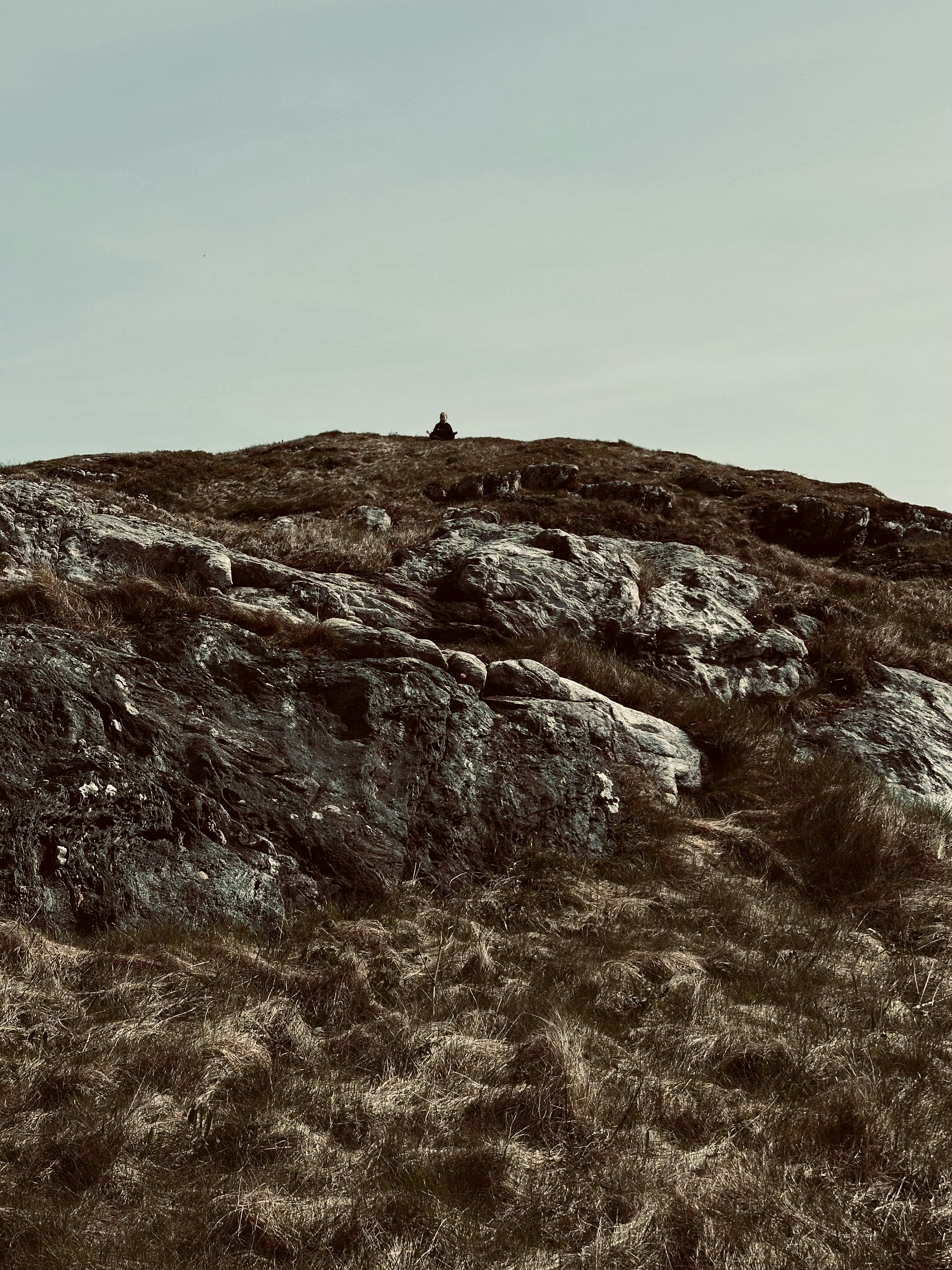 A lone figure atop weathered rocks under a pale sky