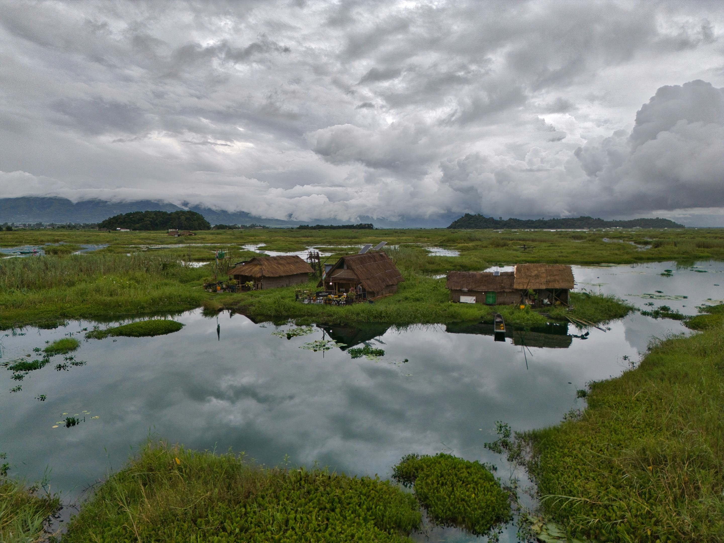 Floating houses in a green lake under a cloudy sky.