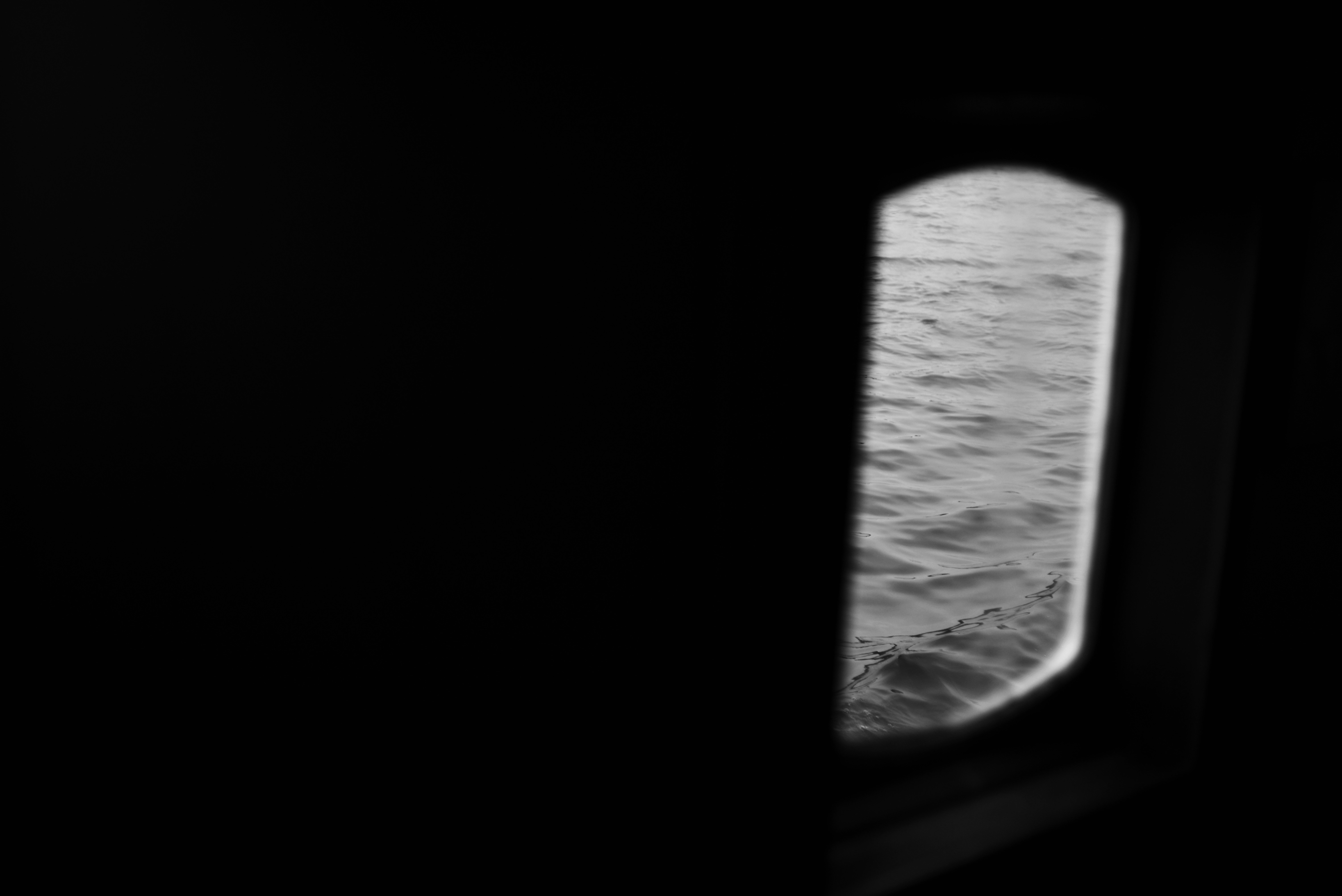 A narrow porthole reveals churning sea beyond a dark cabin