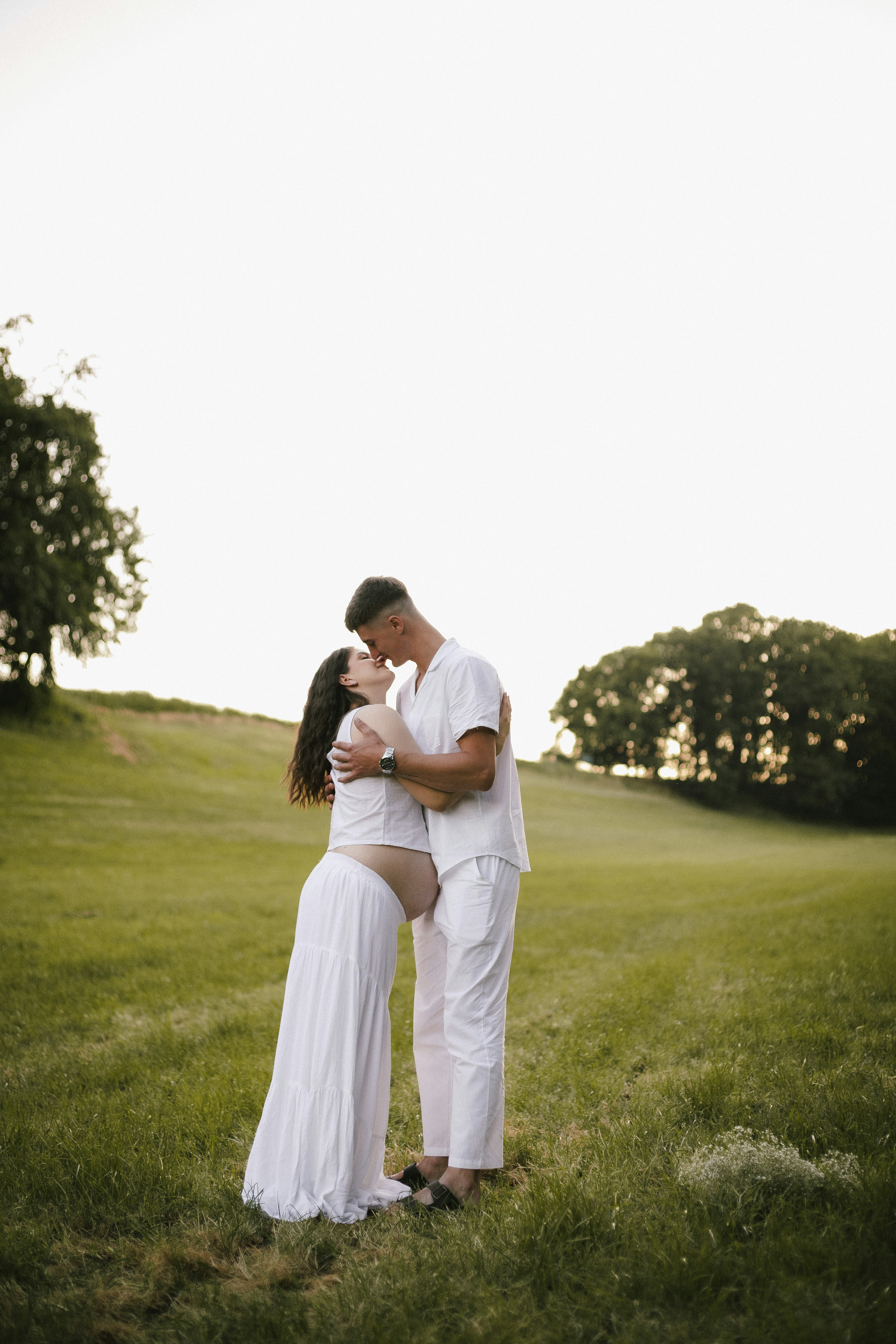 Embrace on the Hill: White Attire in Soft Golden Light