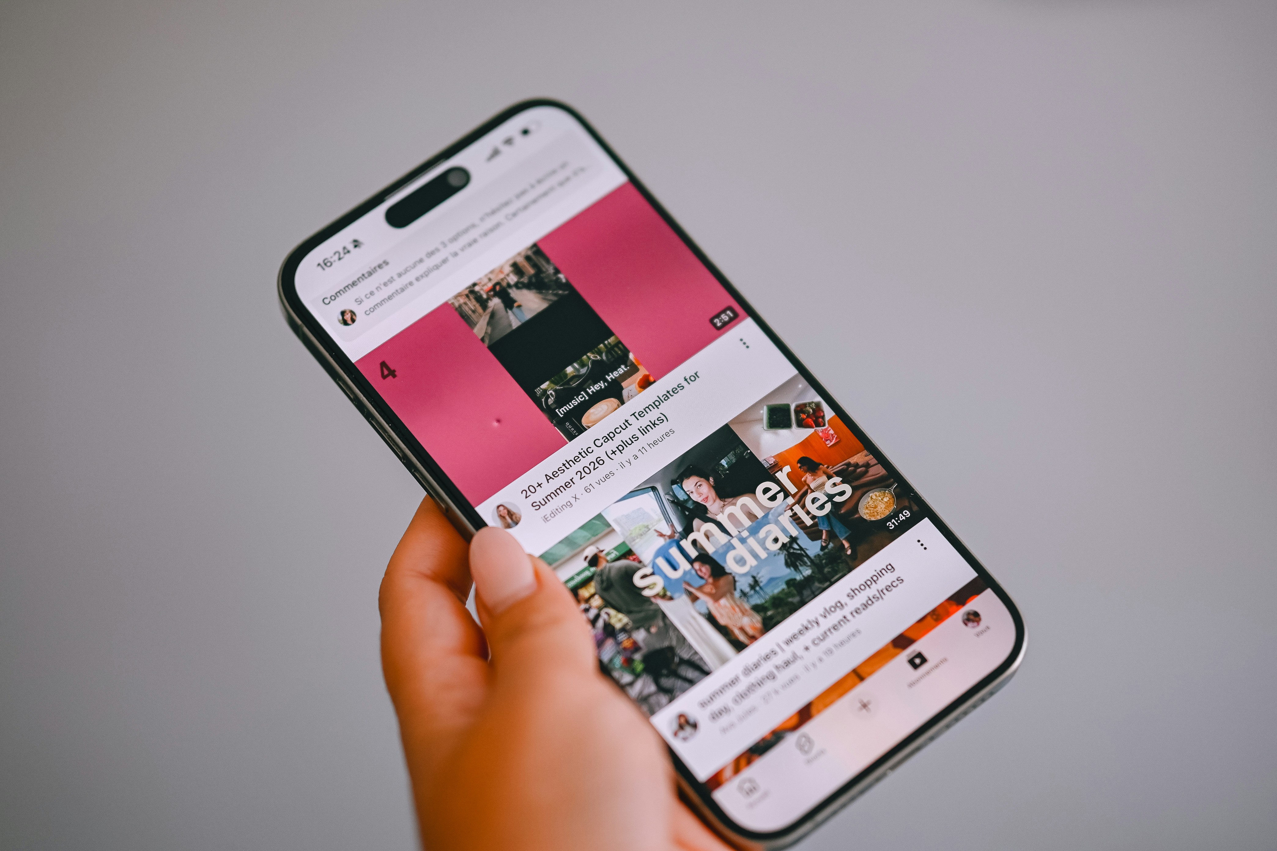 Hand holding a smartphone displaying a streaming app with colorful thumbnails and a pink accent area.
