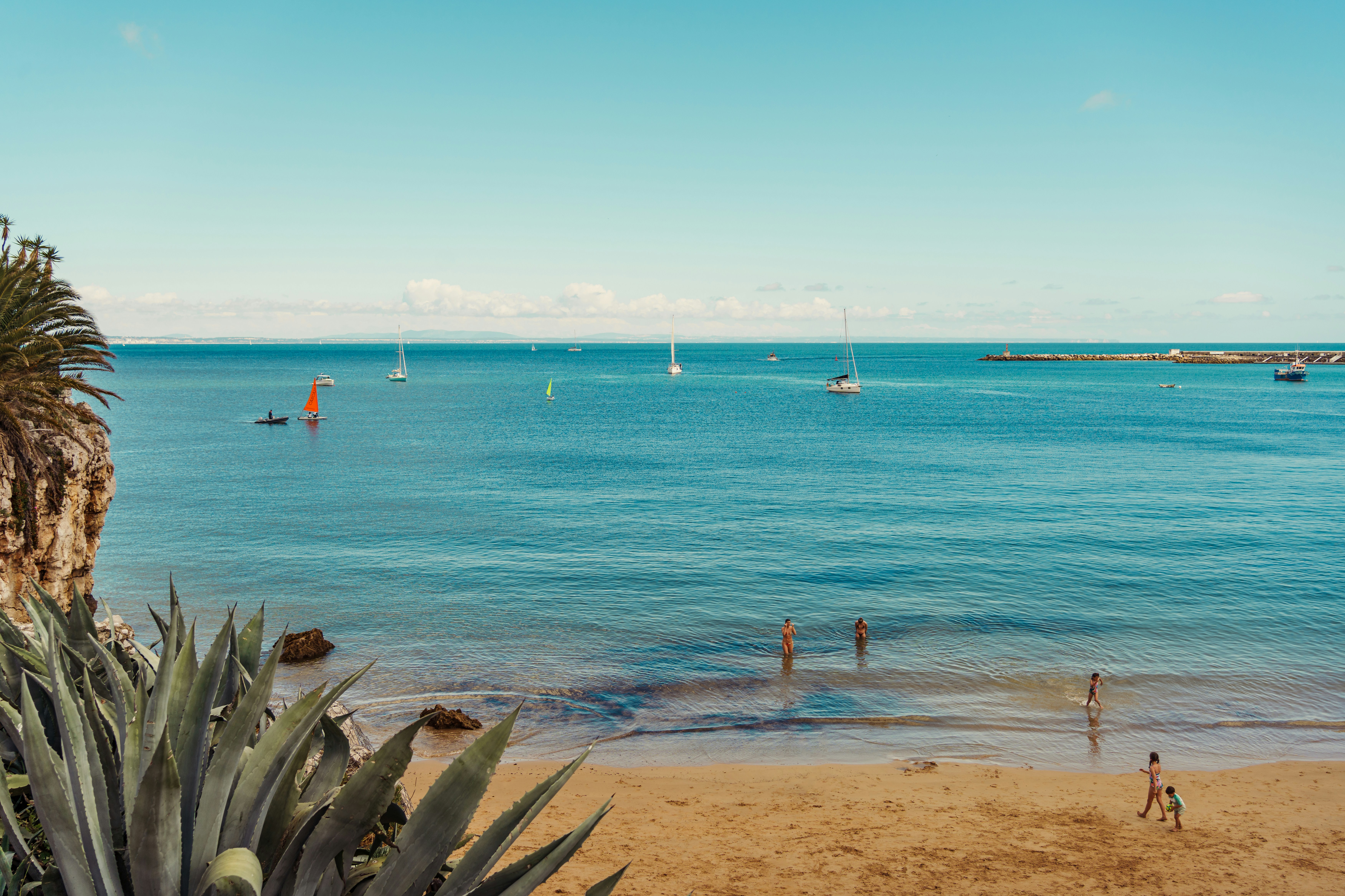 Coastal Tranquility: Sailboats and Surf at a Sunlit Beach