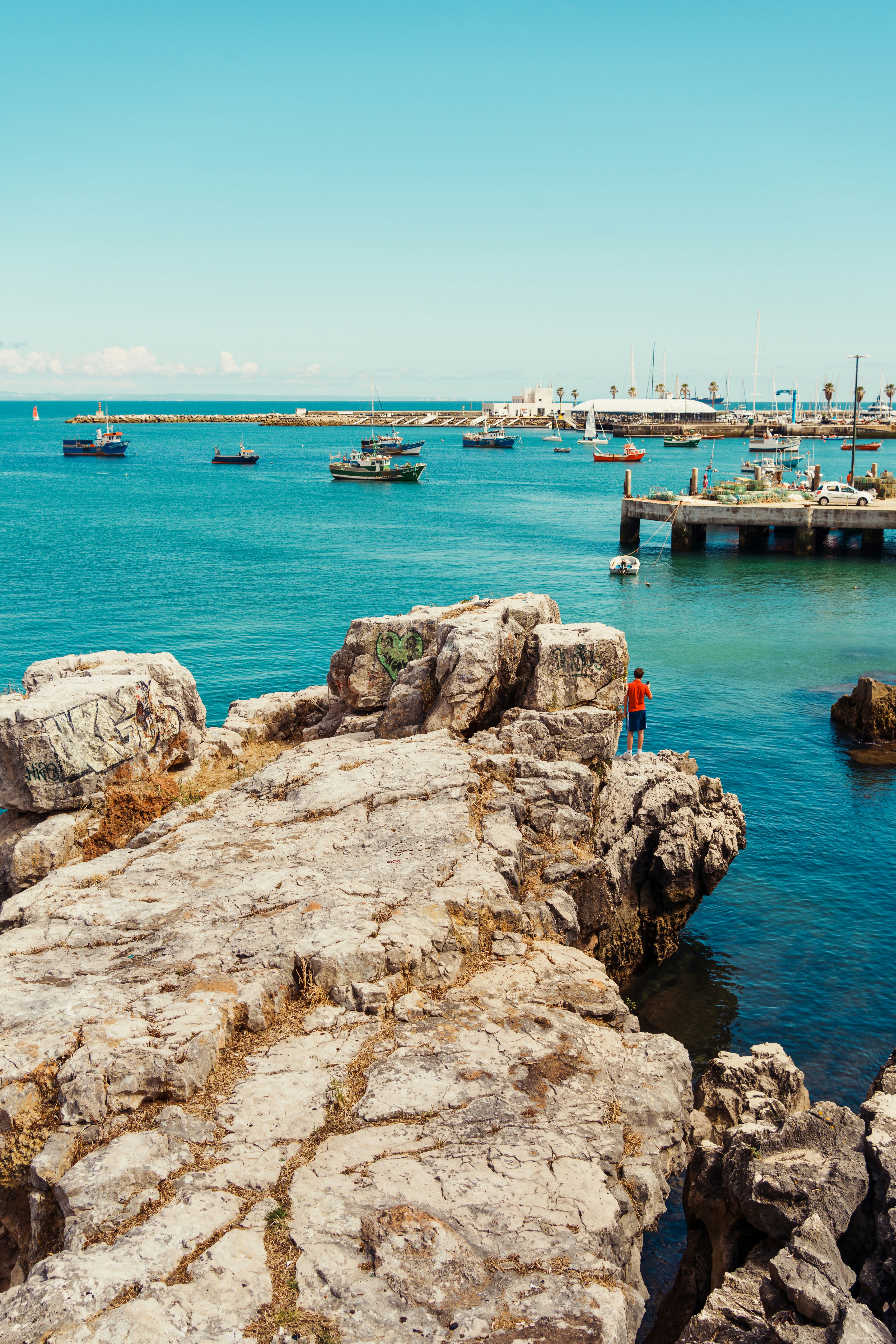 Cliffside Harbor: A Lone Angler Among Teal Waters