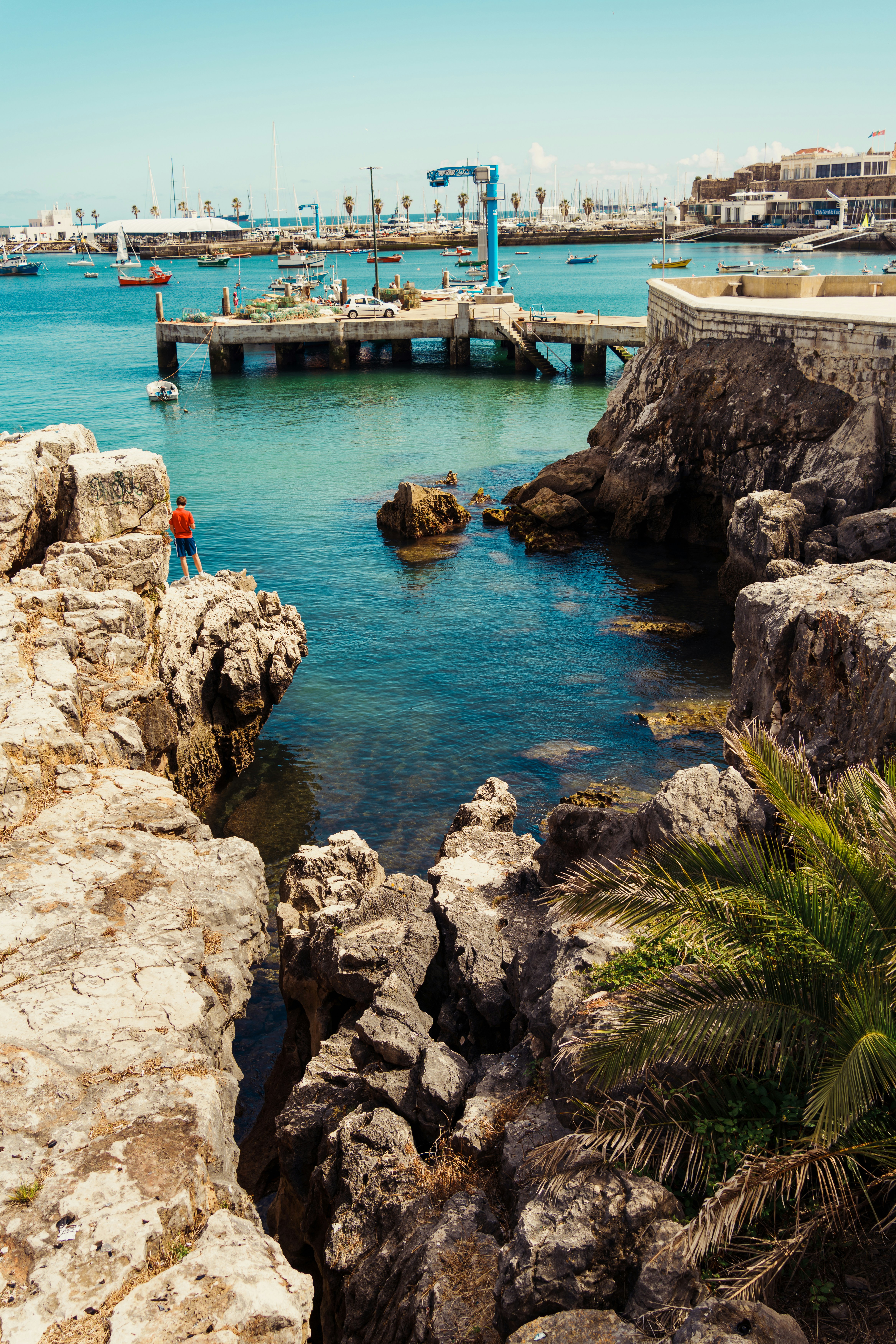 Harbor Edge: A Lone Fisherman Above Turquoise Crevices
