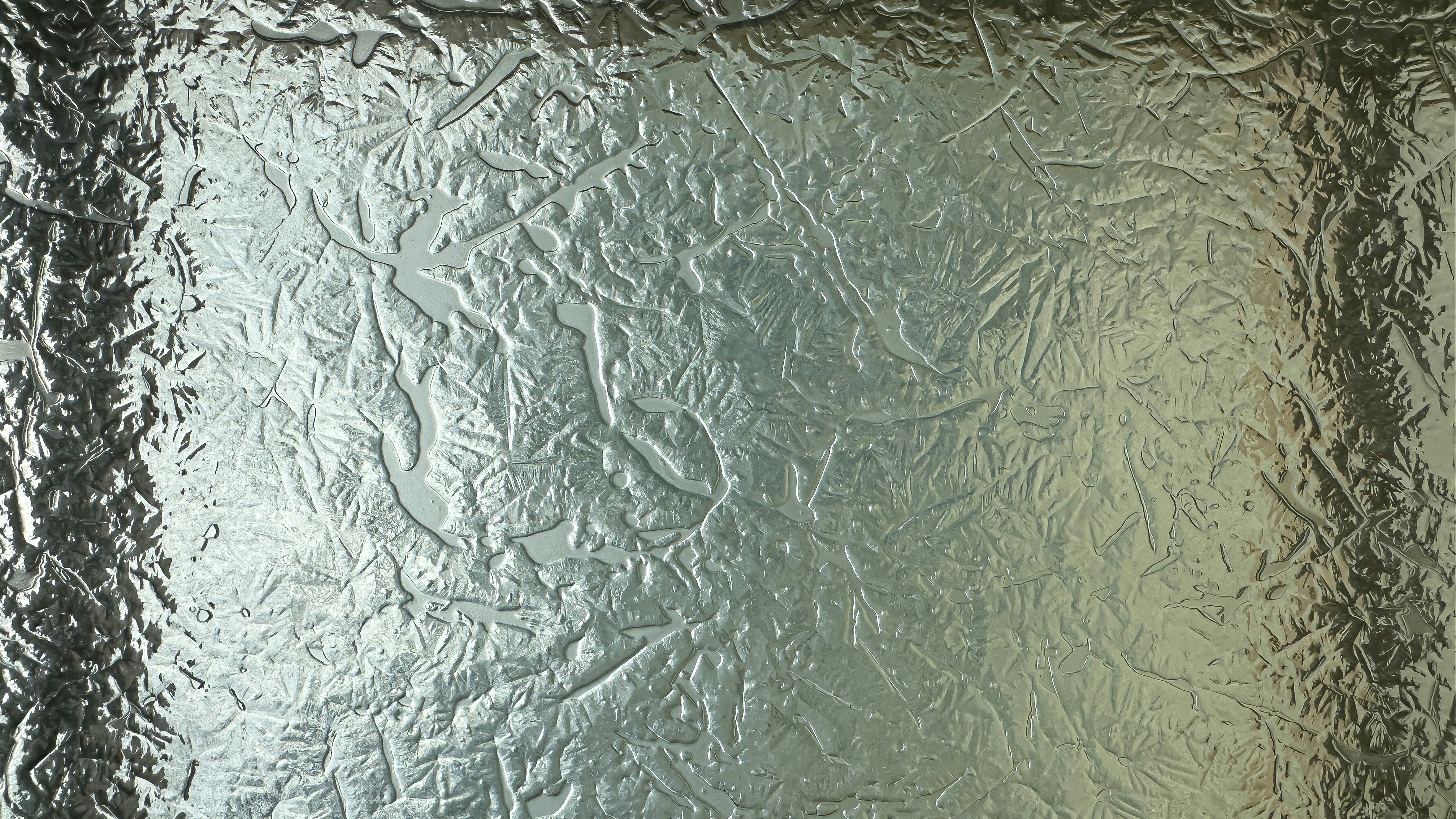 Glossy textured surface with irregular wrinkles and subtle gradient highlights, resembling crinkled foil or glass. A close-up detail emphasizing surface pattern and light play.