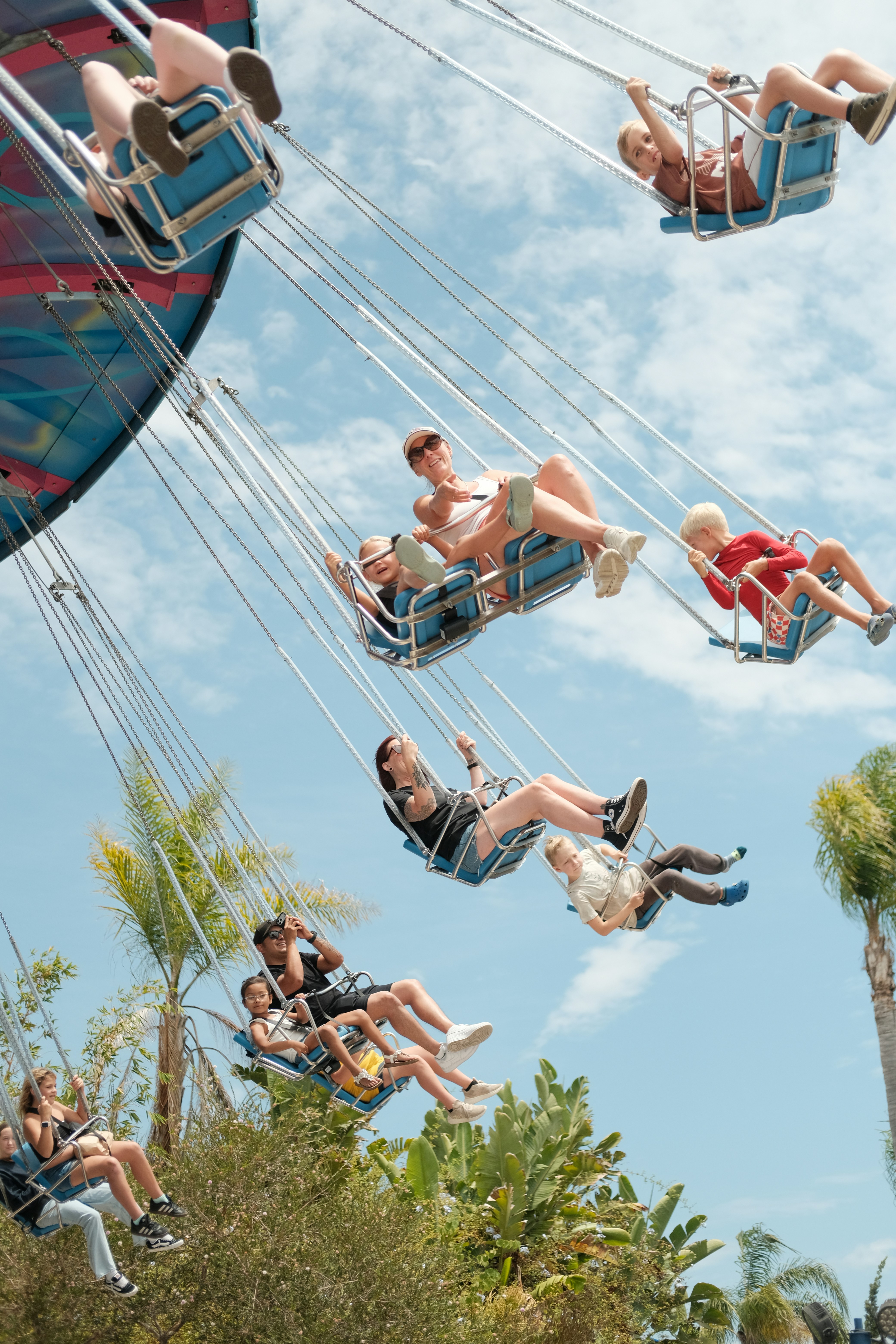 Bright riders on a looping amusement ride suspended against a clear blue sky, captured in vibrant colors and dynamic perspective. This is a candid shot from a theme park, not a painting or logo.