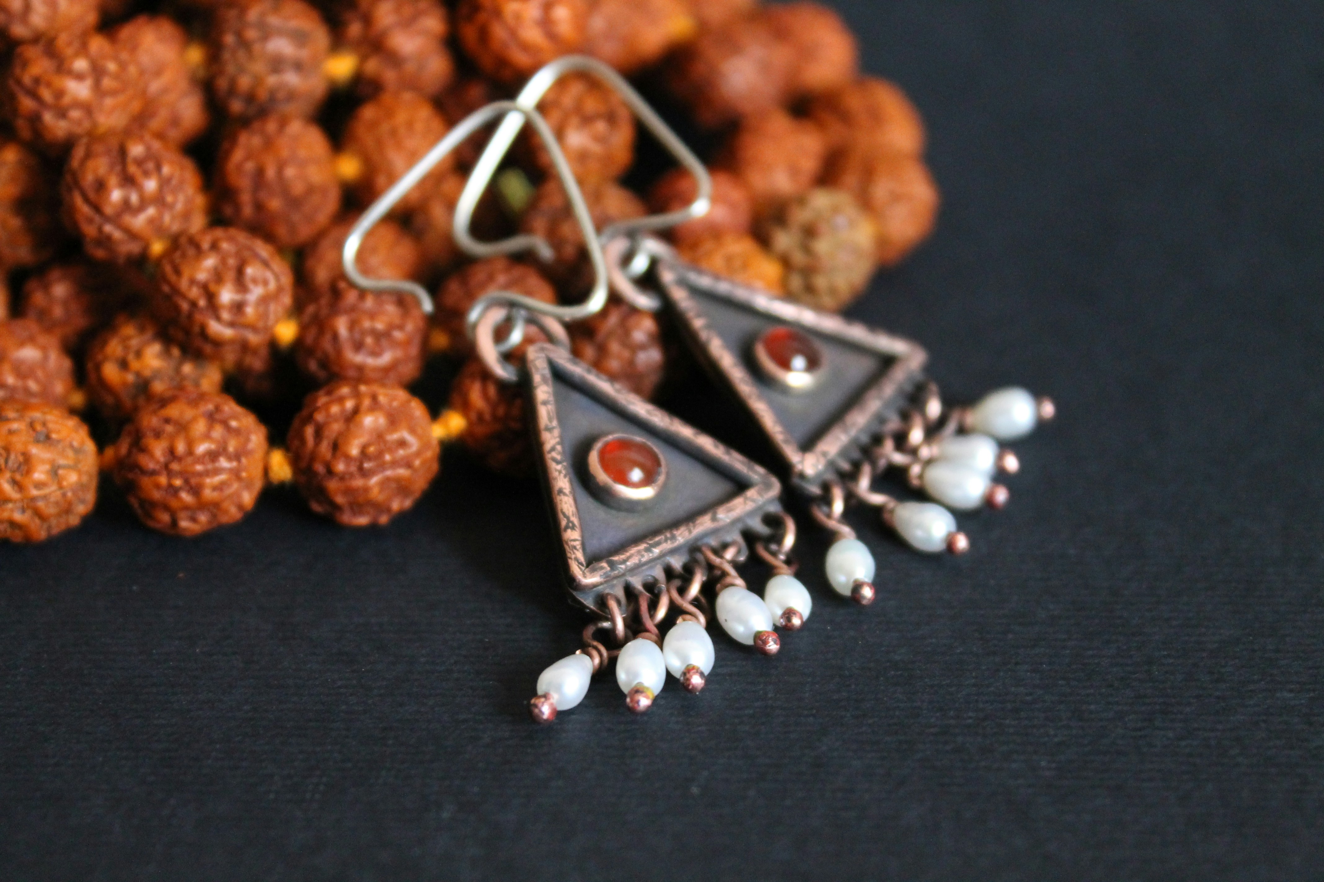 Geometric earrings resting on dried beads against a charcoal backdrop