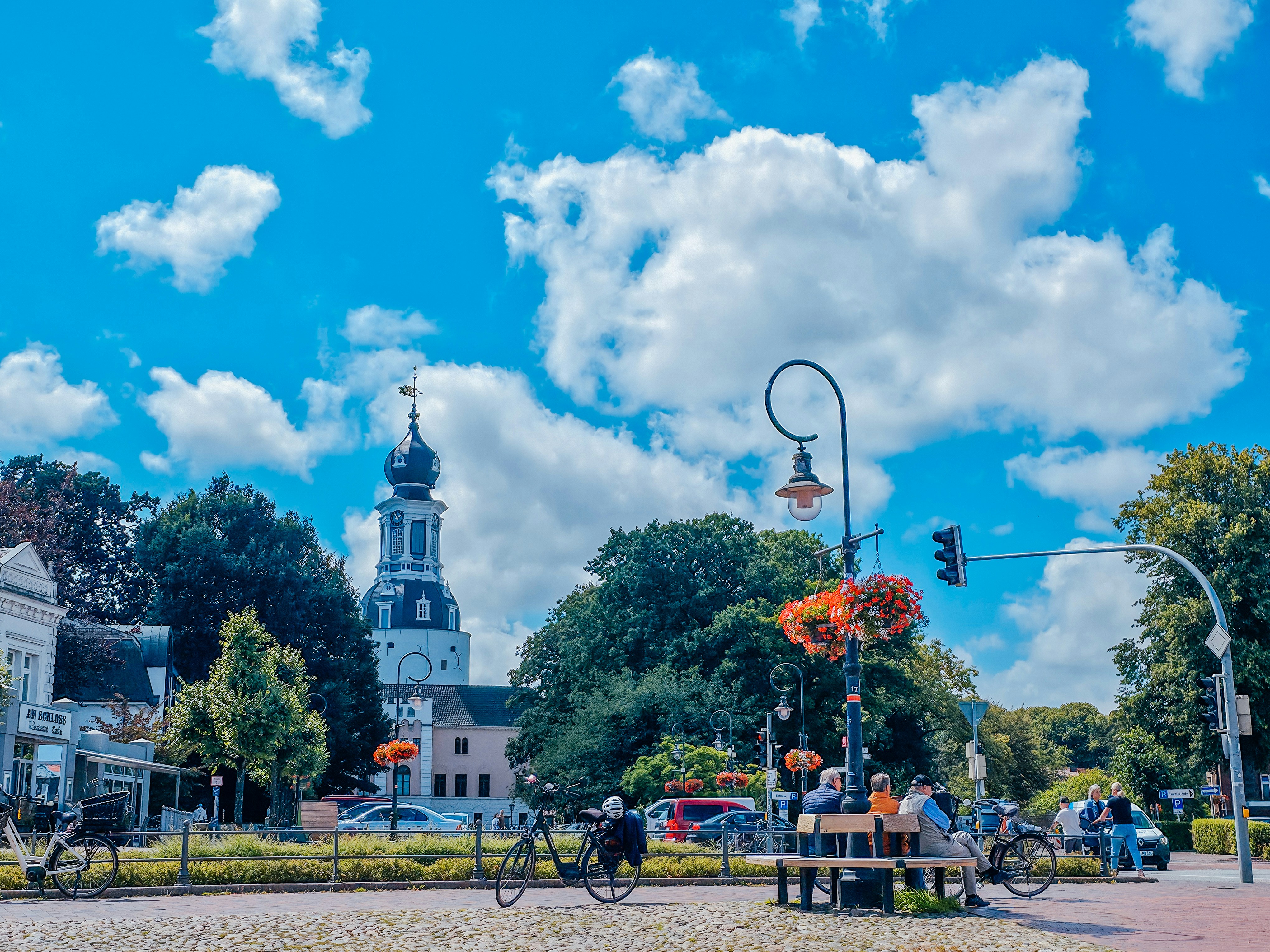 Clock tower, cafe, and river-town bustle under a bright blue sky