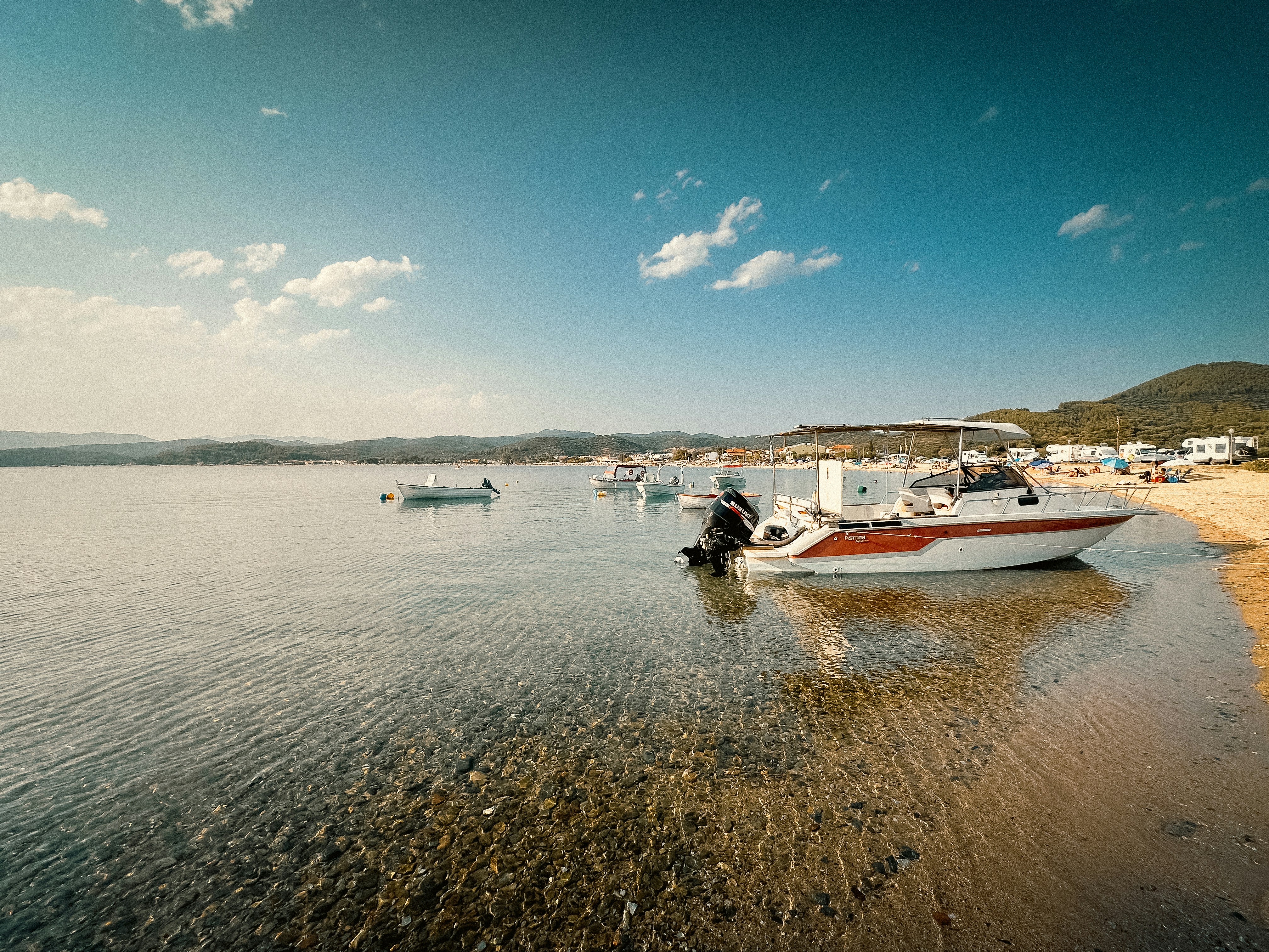 Small boats rest along the crystal-clear shoreline of Toroni Beach in Sithonia, Halkidiki, Greece. Calm Mediterranean waters, golden sand, and distant hills create a peaceful summer scene on one of northern Greece’s most beautiful beaches.