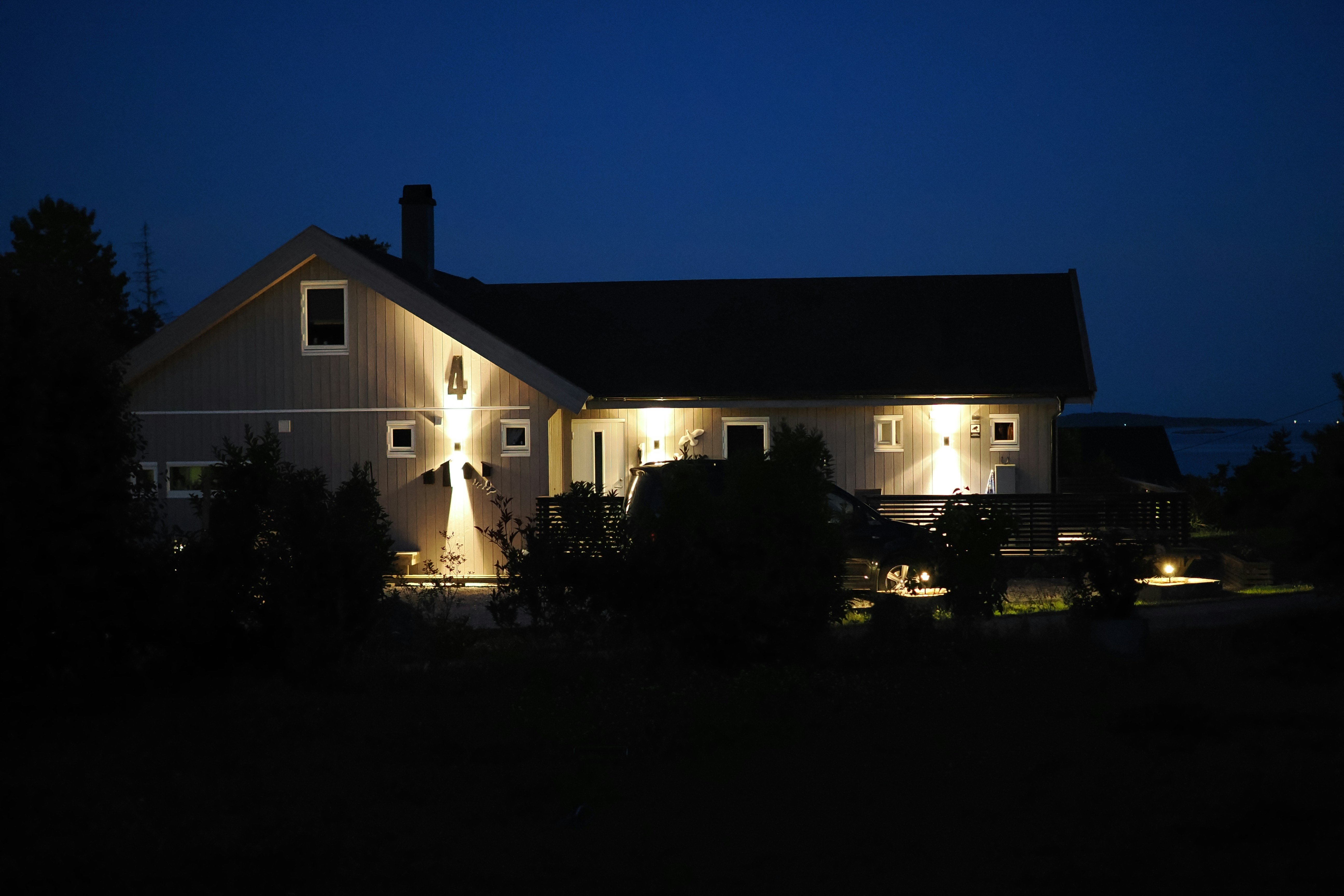 A quiet lakeside lodge bathed in warm exterior lights at night, with silhouettes of trees and a dark shoreline.