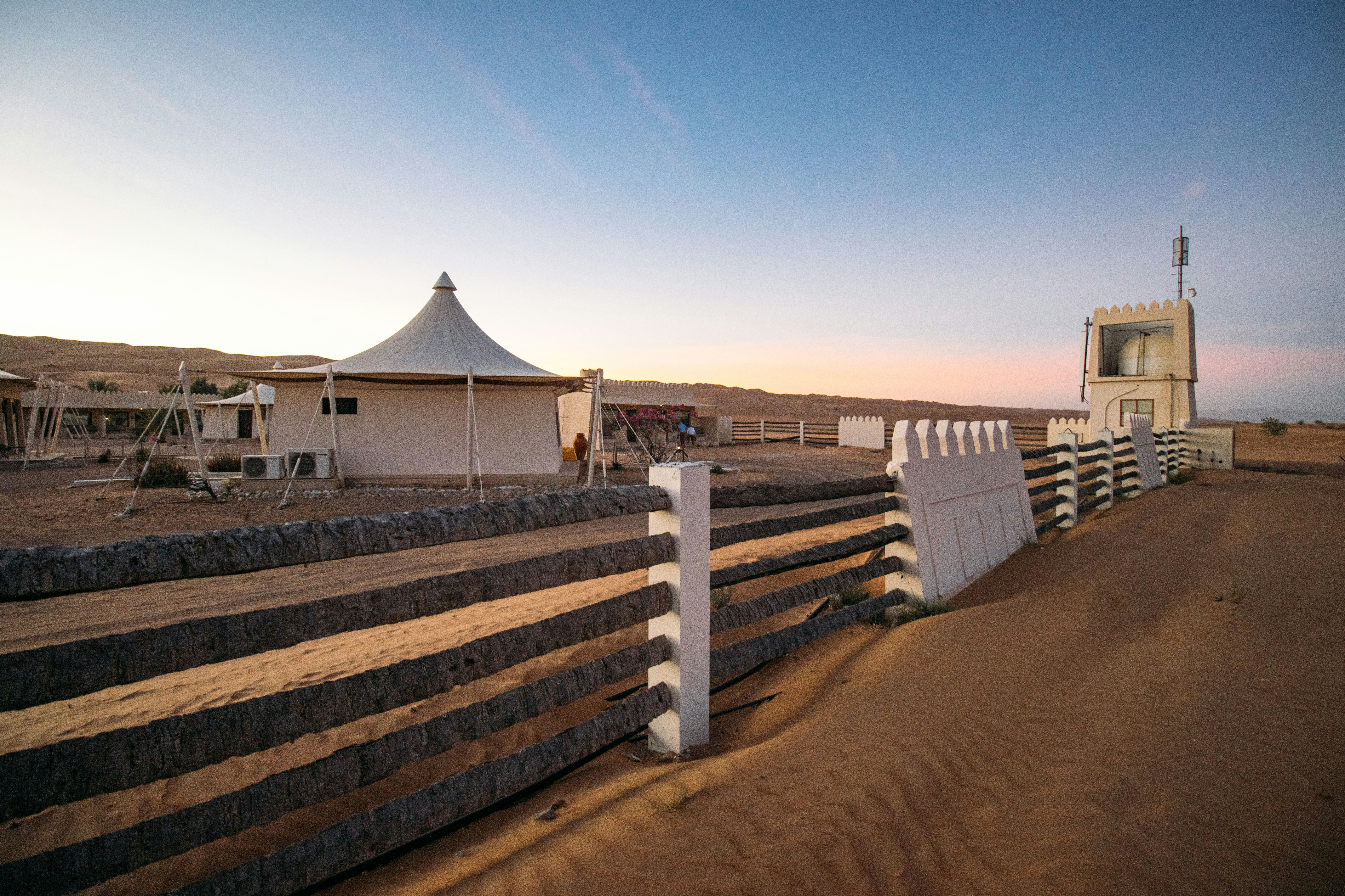 Desert Camp at Dusk: Tents, Fence, and Watchtower in Soft Light