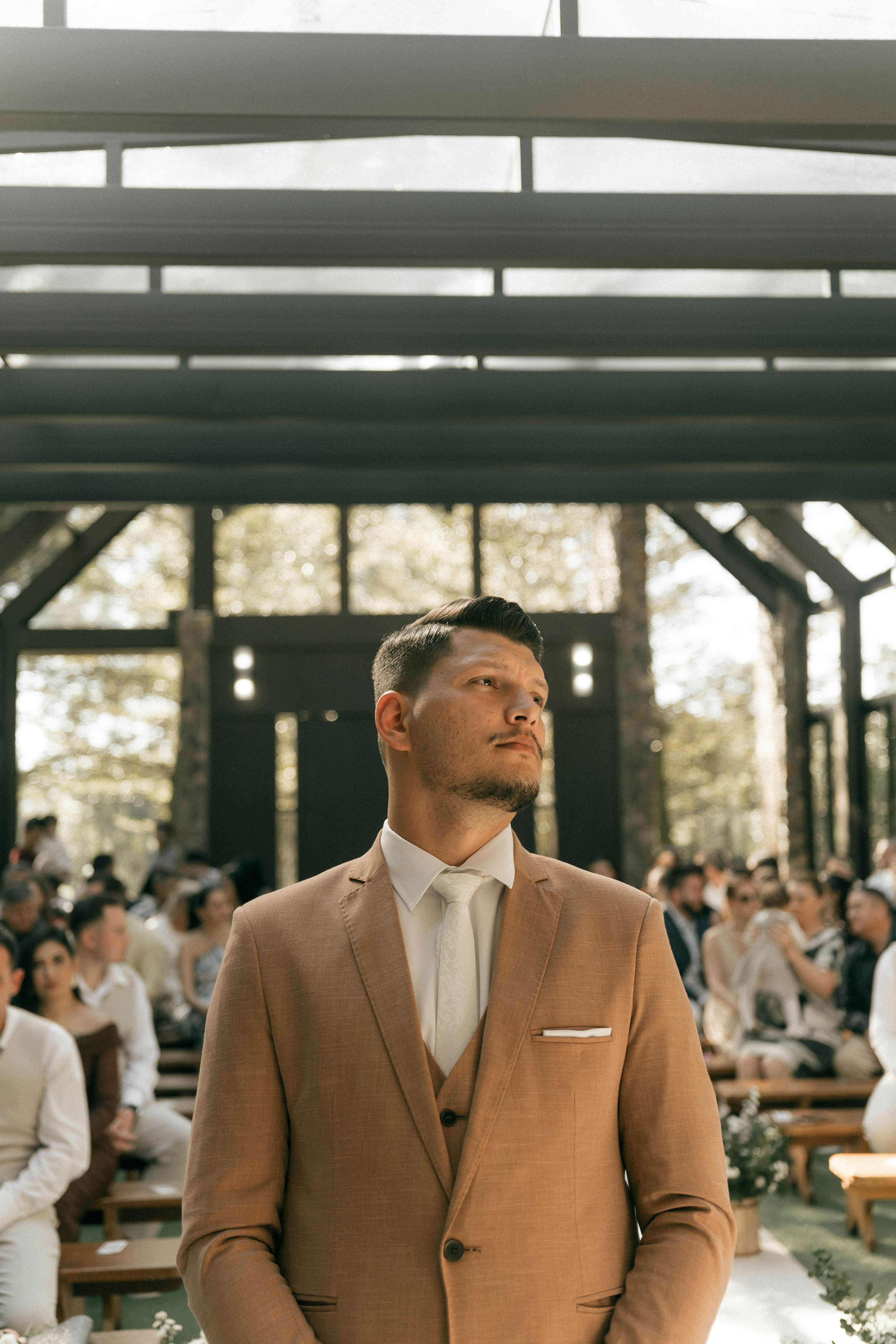 Groom in tan suit overlooking the aisle amid wedding guests