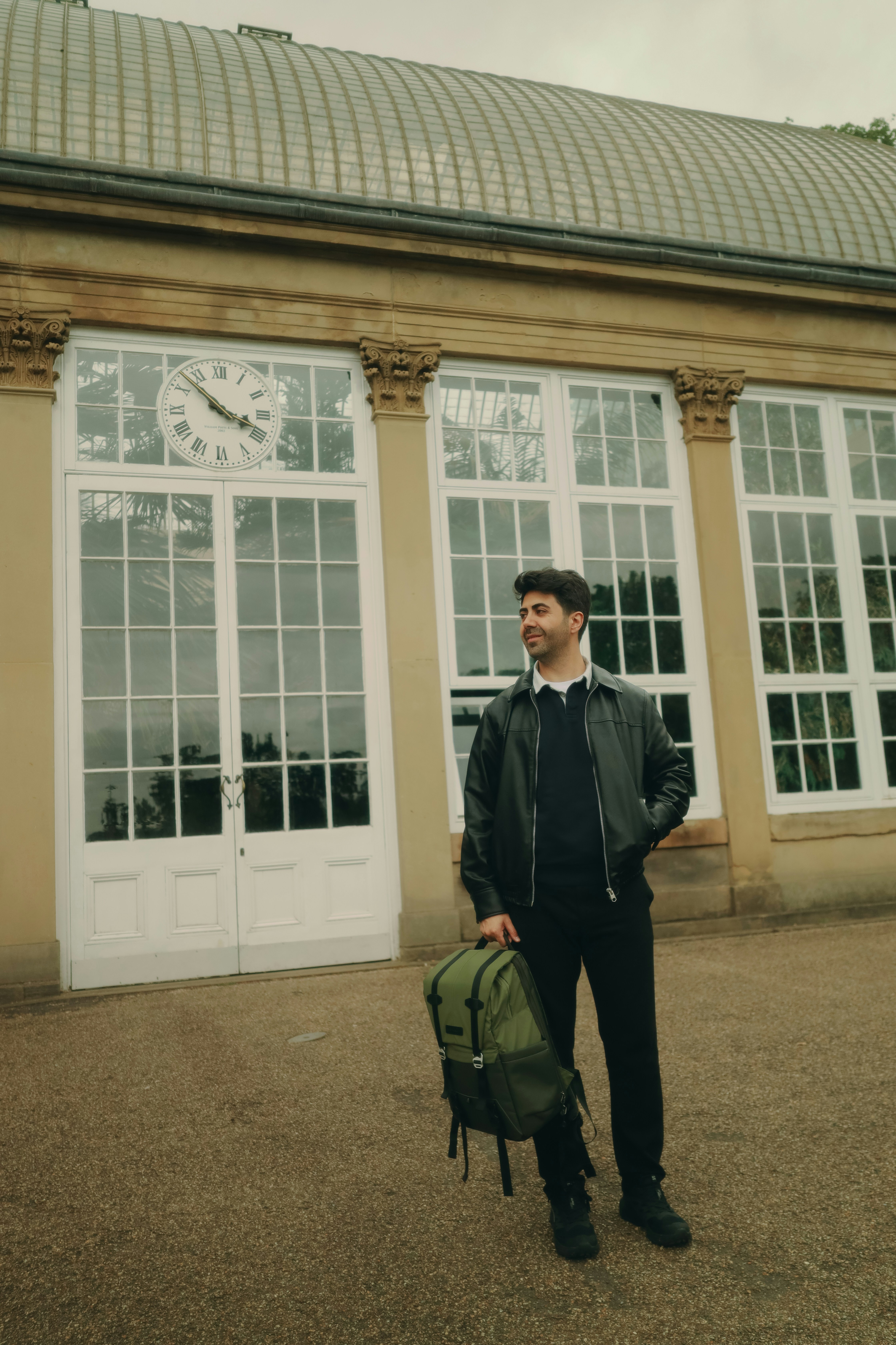Traveler with a Green Backpack Stands Before a Classical Glass Conservatory Clock