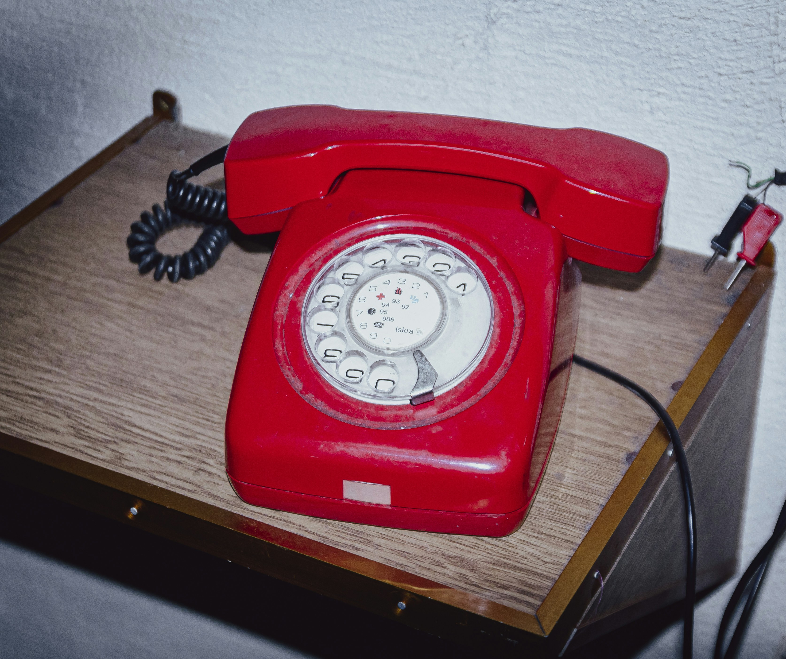 Crimson Classic: A Retro Rotary Phone Resting on a Wooden Nightstand