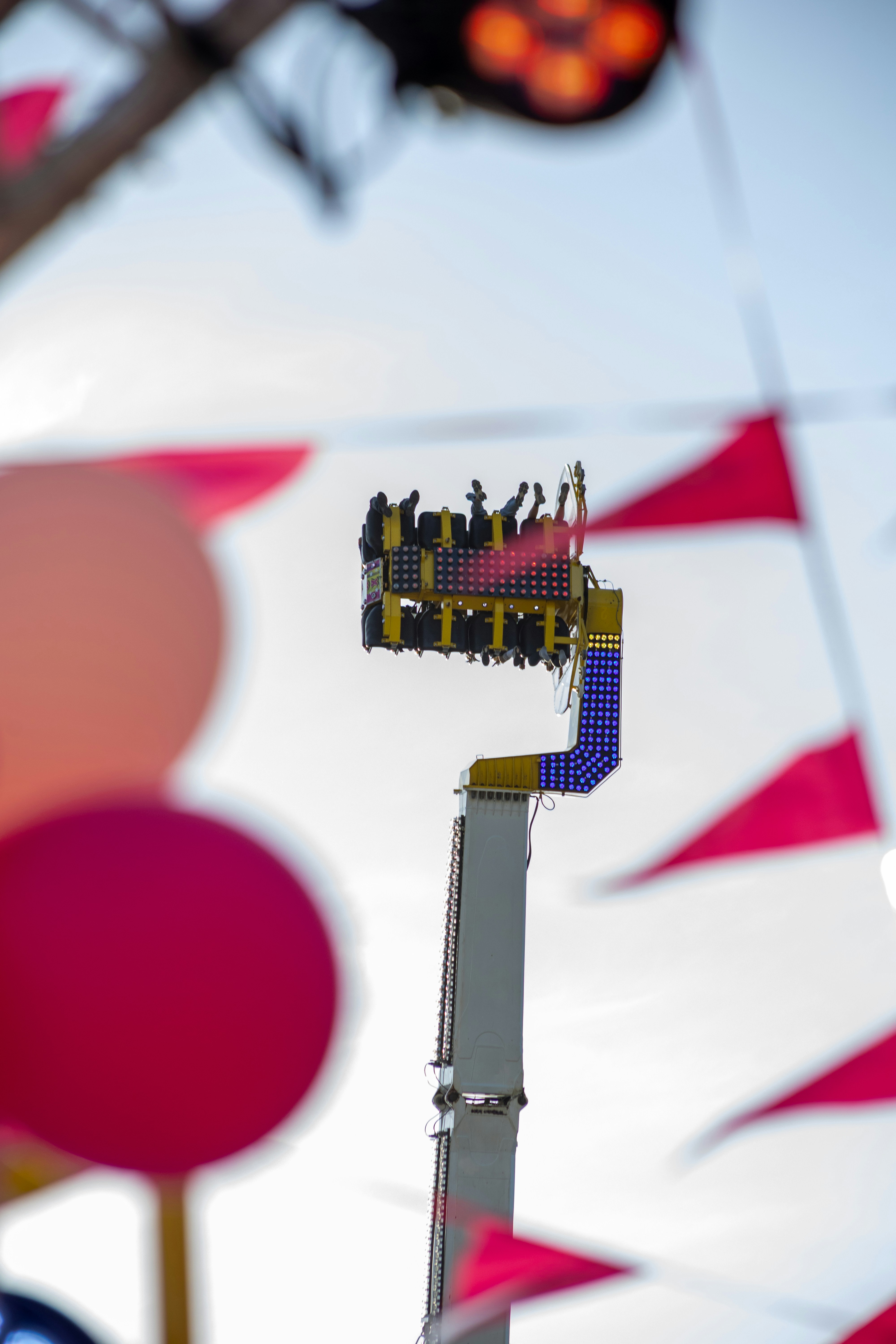 Tall amusement-ride lights sit against a bright sky, with festive pink balloons and pennant banners framing the scene for a candid carnival moment.