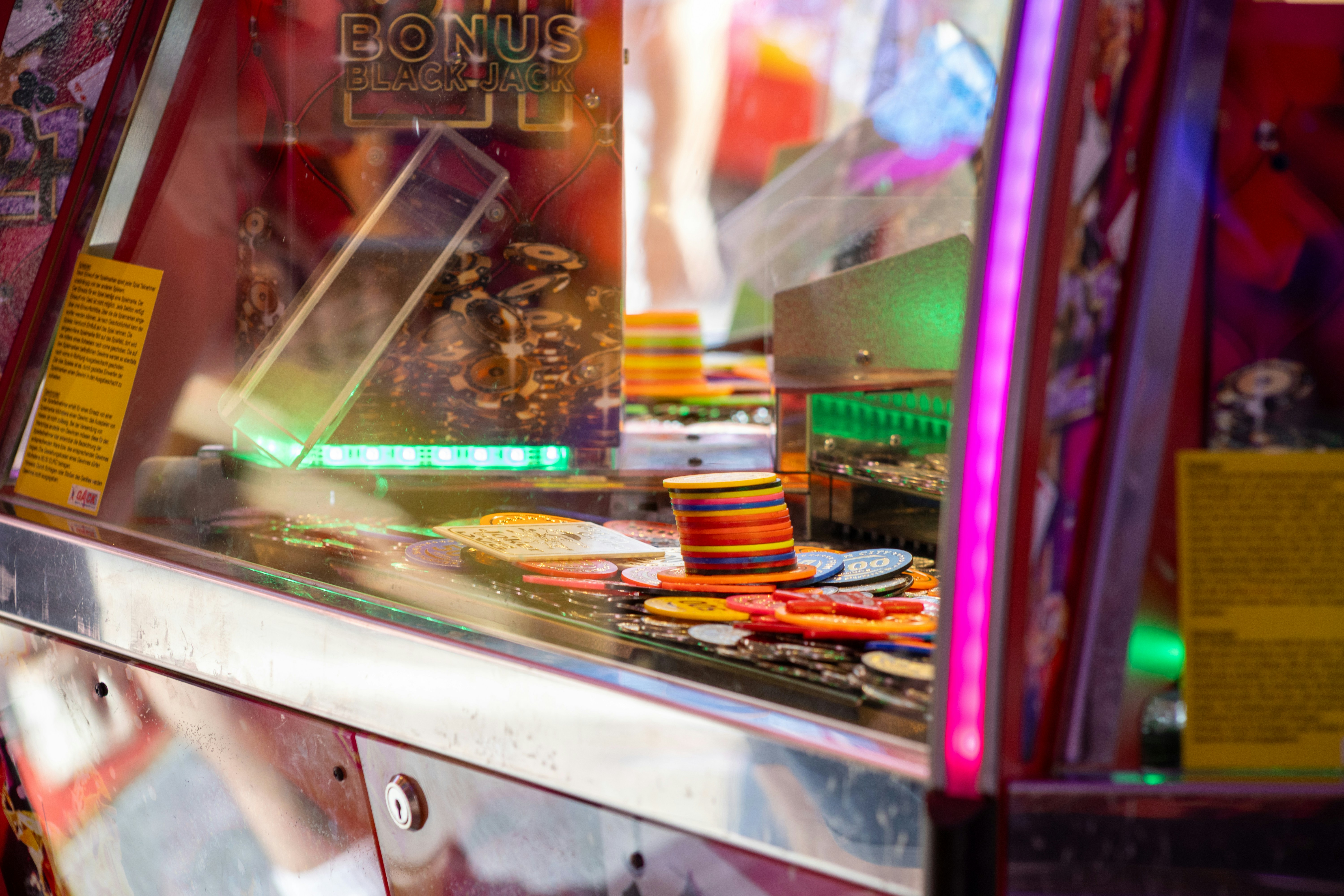 Colorful arcade prize booth with stacked chips and neon lights; metallic surfaces reflect vibrant colors and hint at the claw machine’s glass enclosure.