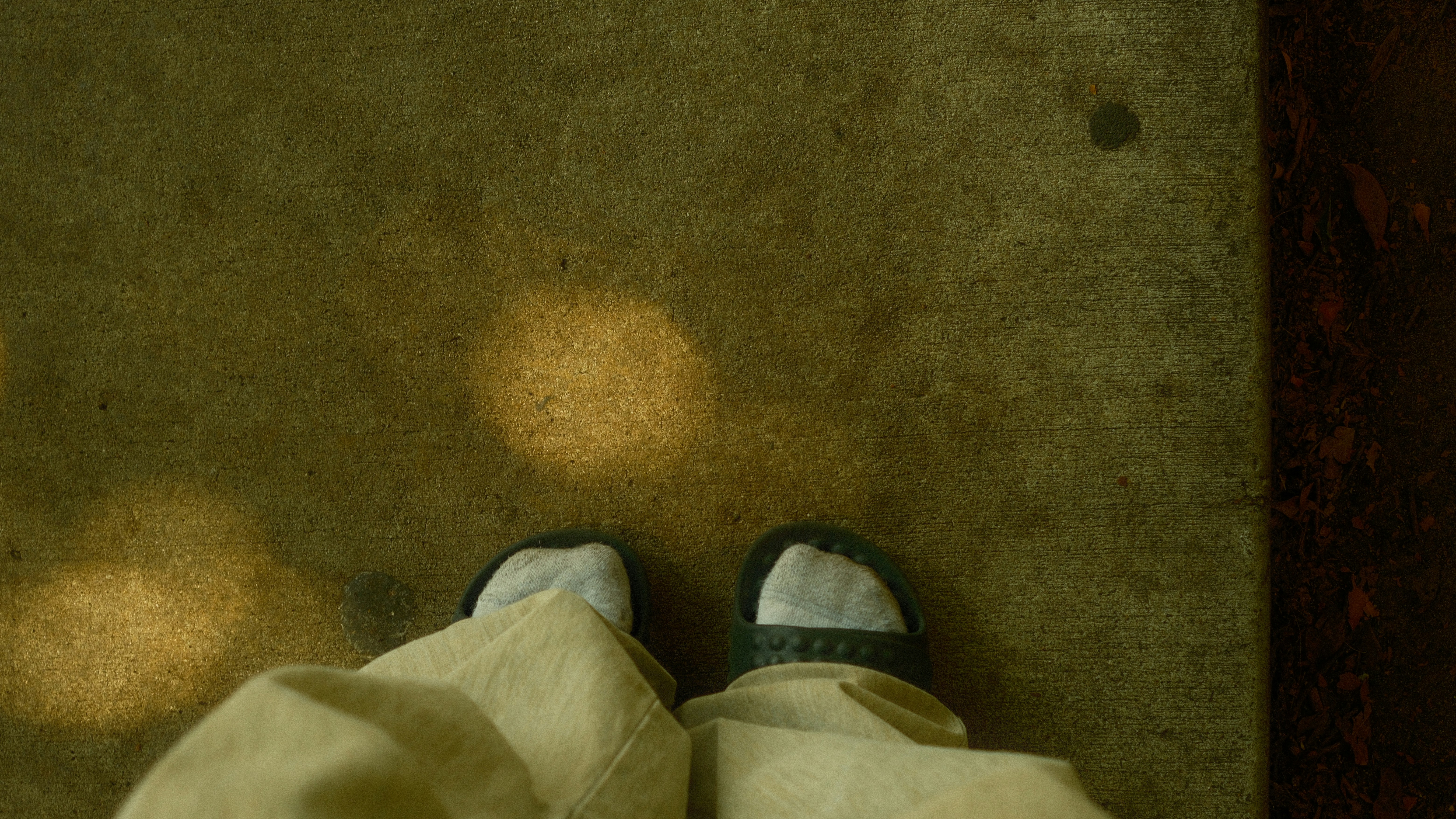 Dimly lit sidewalk with dappled sunlight and a pair of sandals, suggesting a lone wanderer paused mid-step.