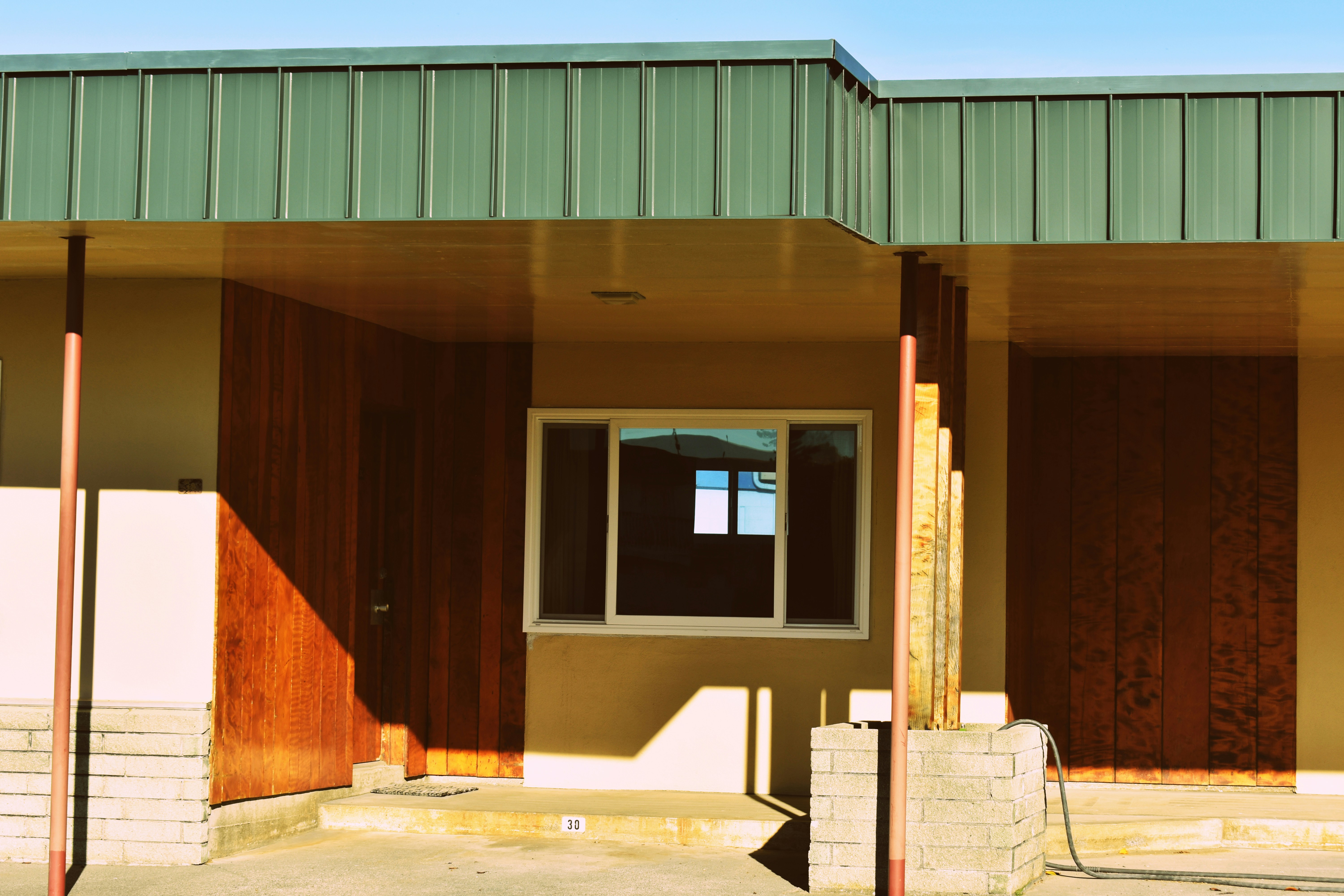 Sunlit storefront with wooden paneling, a central window, and a small step leading to a recessed entrance.