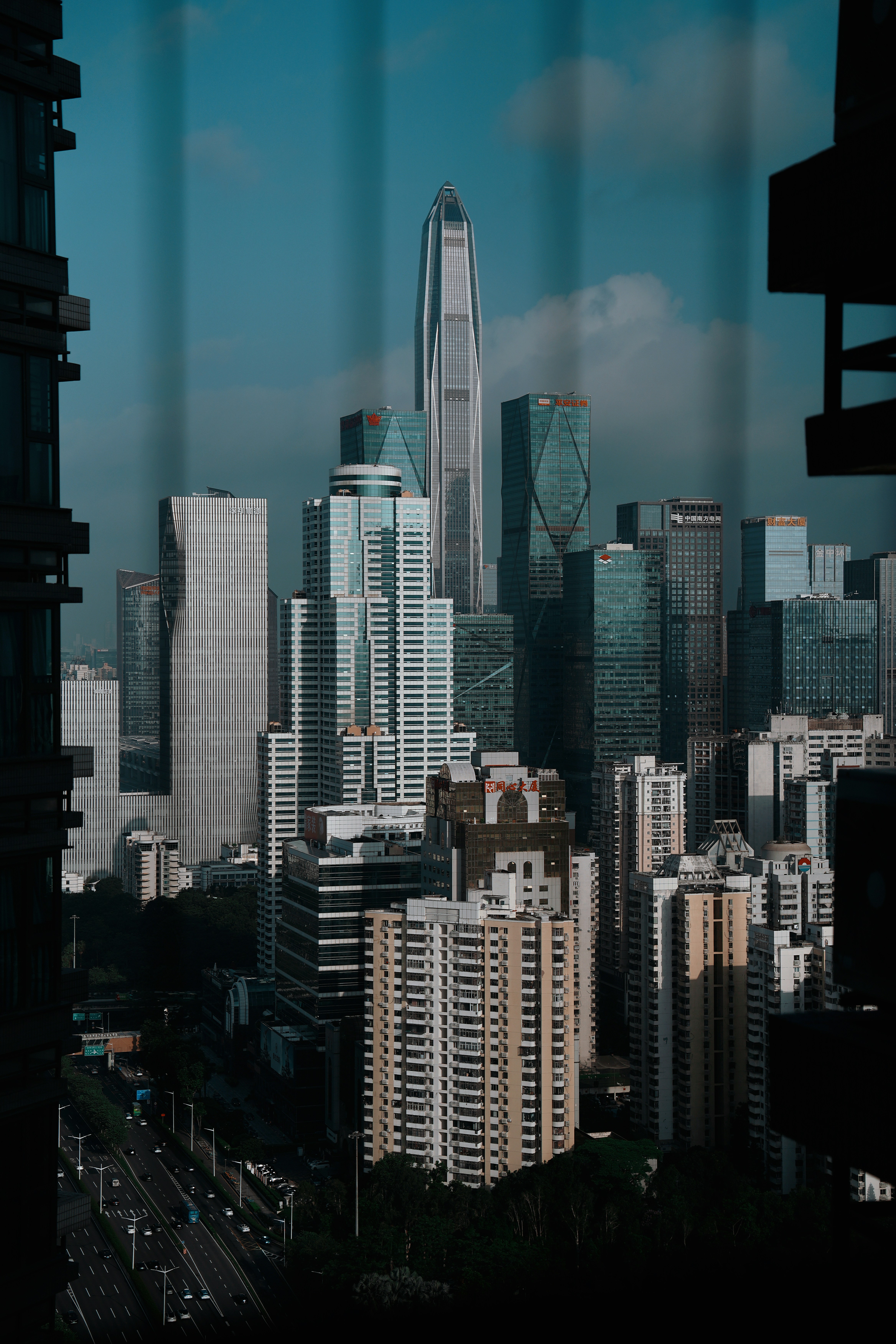 Rising skyline with a slender central tower framed by dense mid-rise buildings, captured from a high vantage as daylight renders cool blues and subtle shadows.