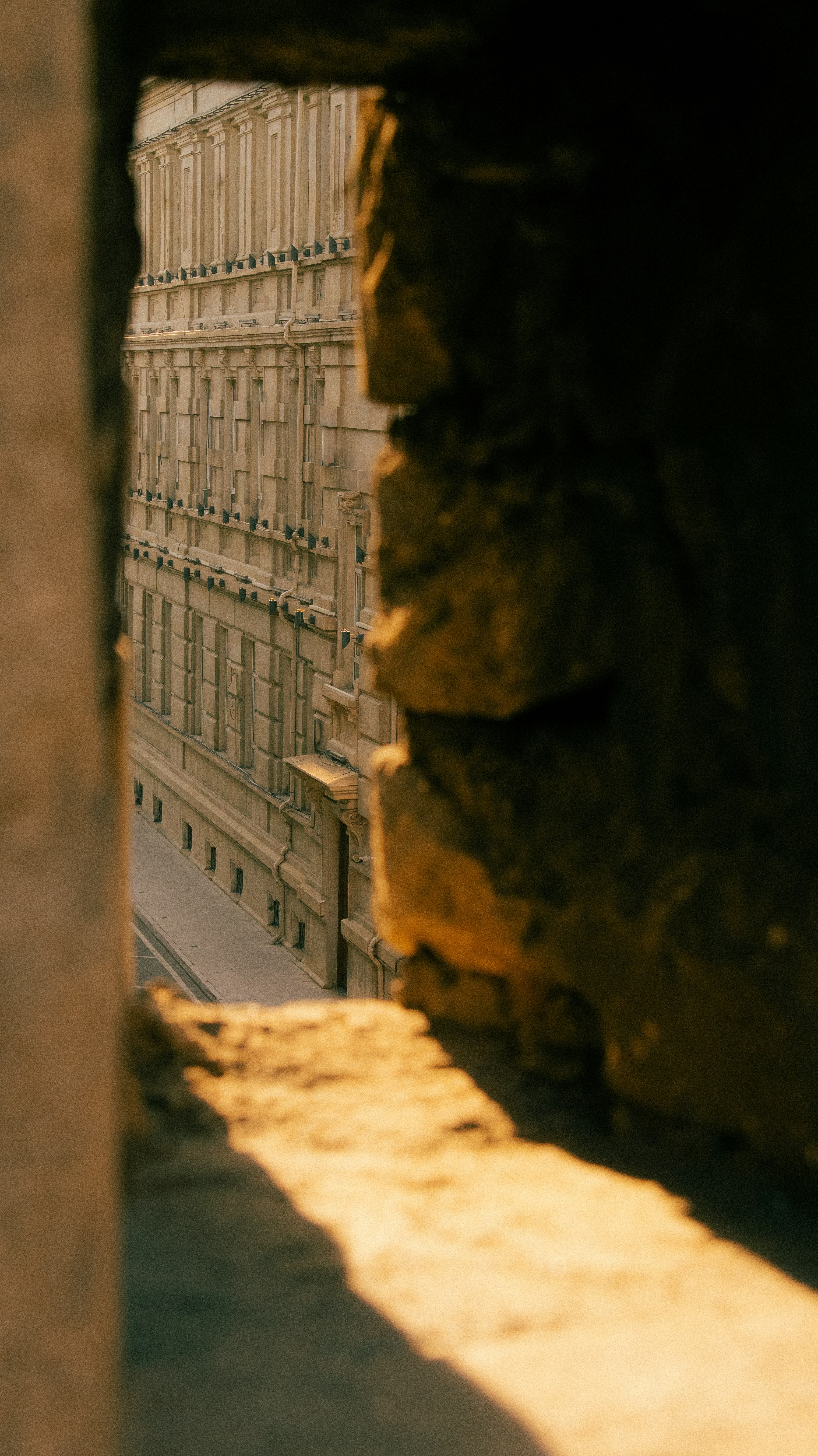 Through a Narrow Aperture: Sunlit Facade Beyond a Framing Wall