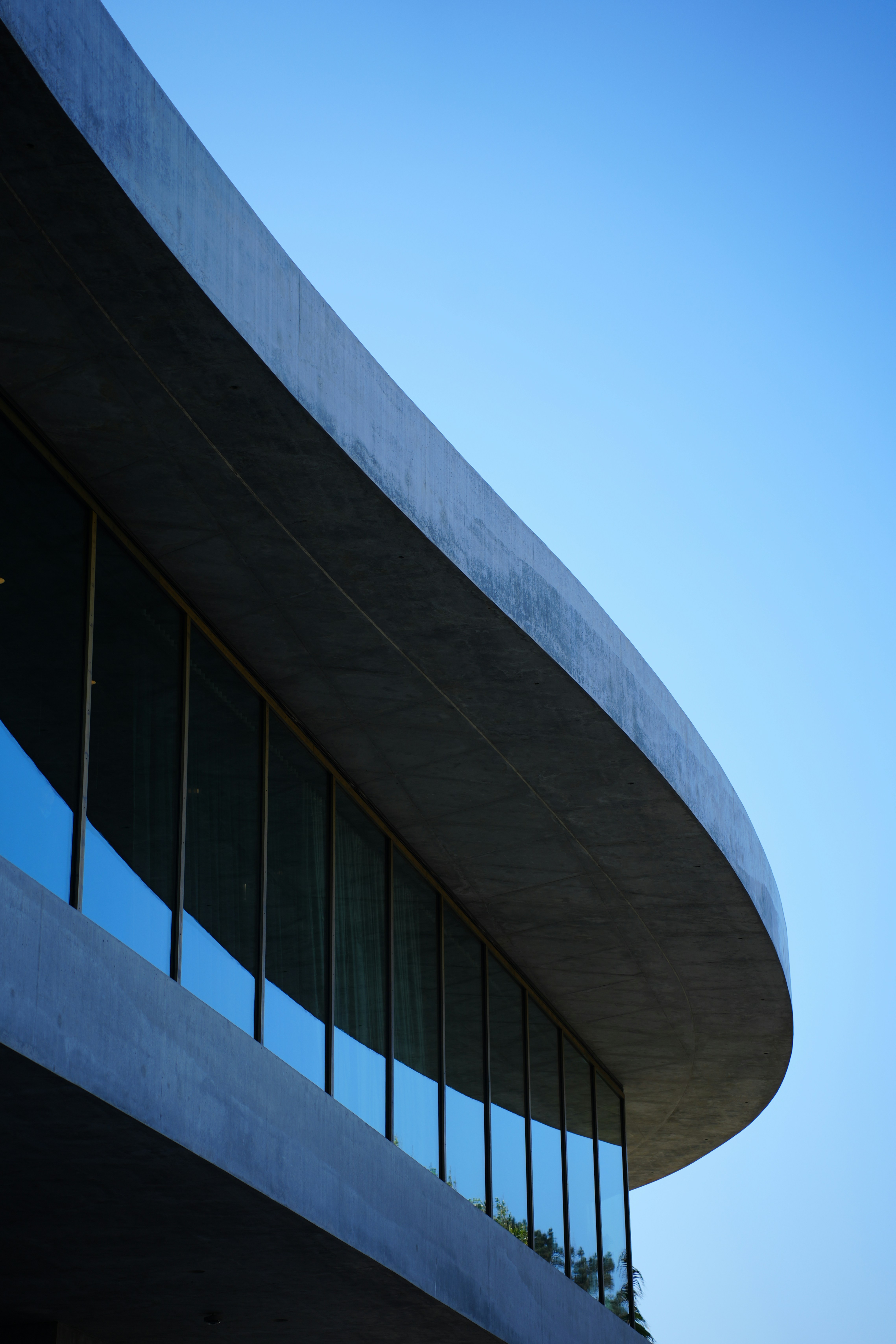 Architectural curve with expansive glass facade against a blue sky, emphasizing clean lines and modernist form.