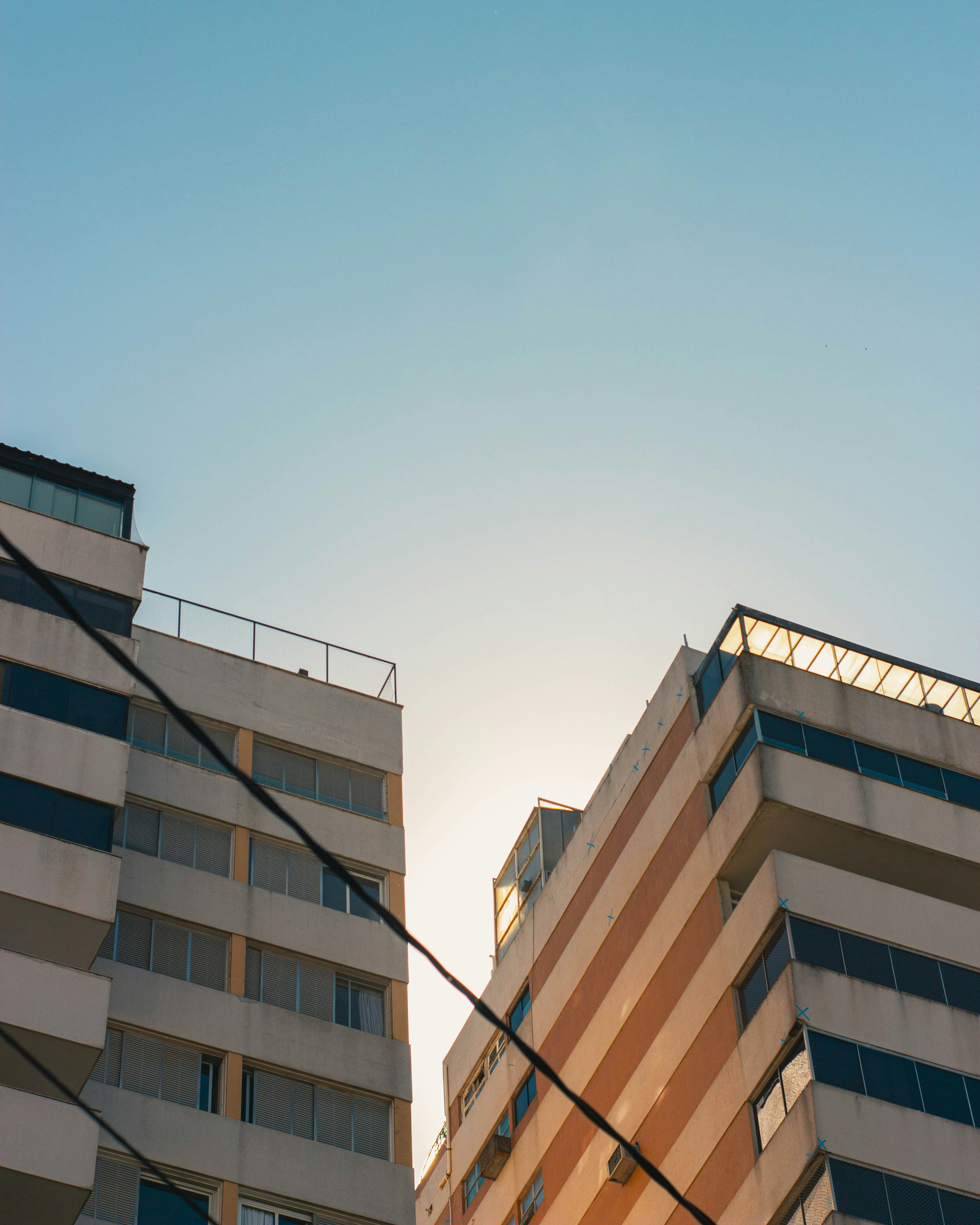 Two modern apartment blocks frame a pale dawn sky, with sunlight catching the edges of the structures.