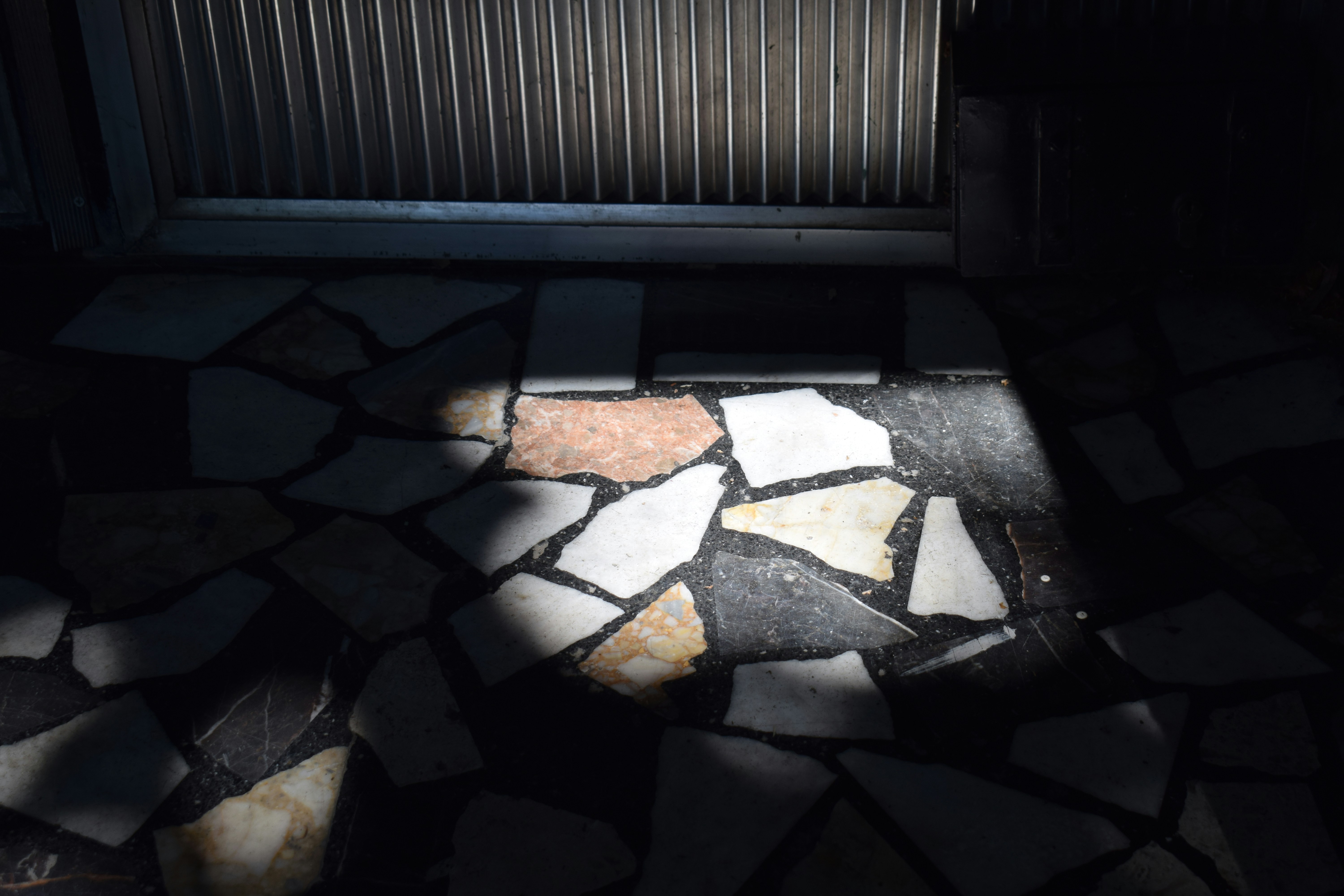 A Narrow Patch of Light on Tiled Ground Near a Closed Gate