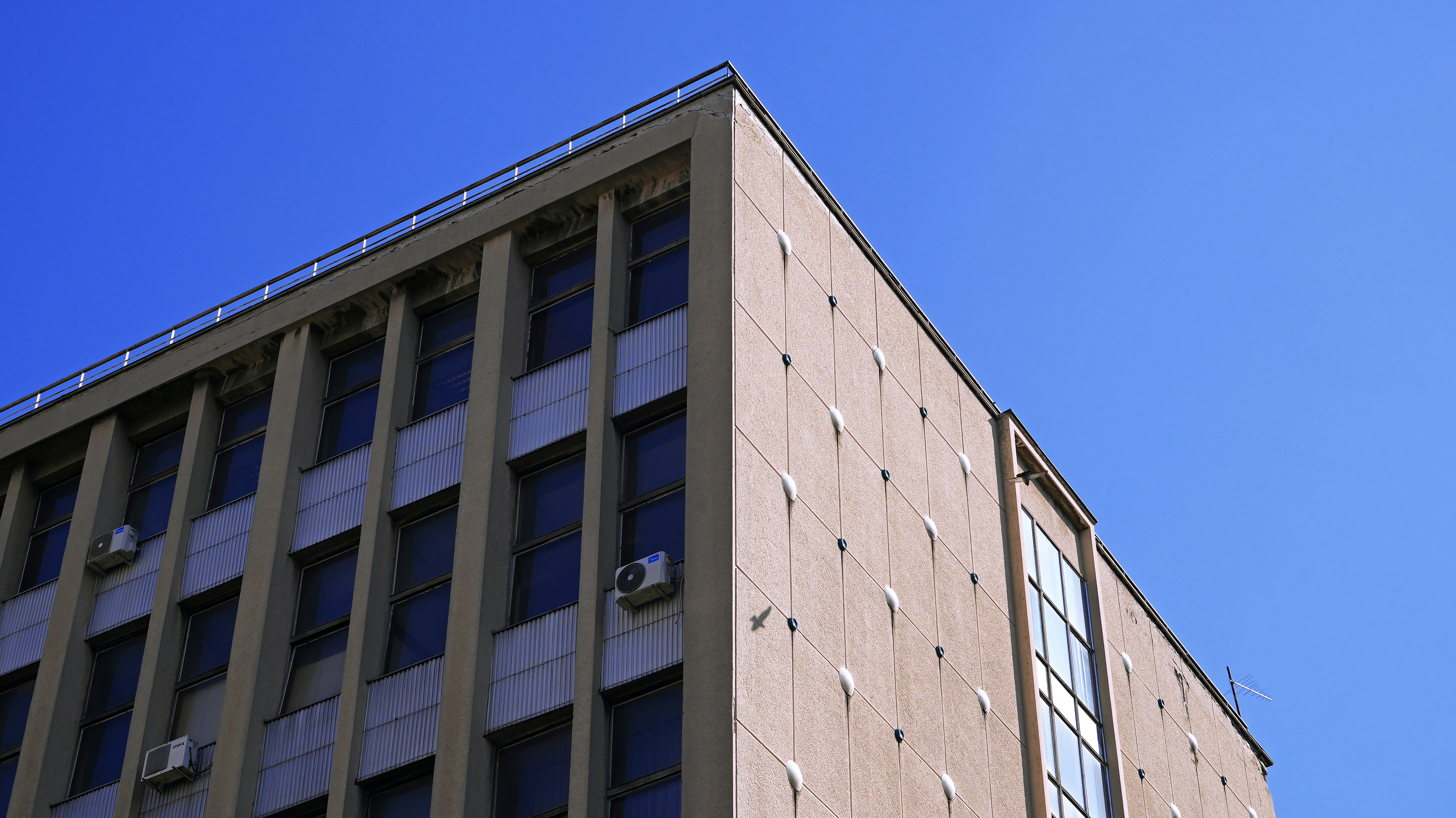 Angular concrete building facade under a vivid blue sky with evenly spaced windows and external units.