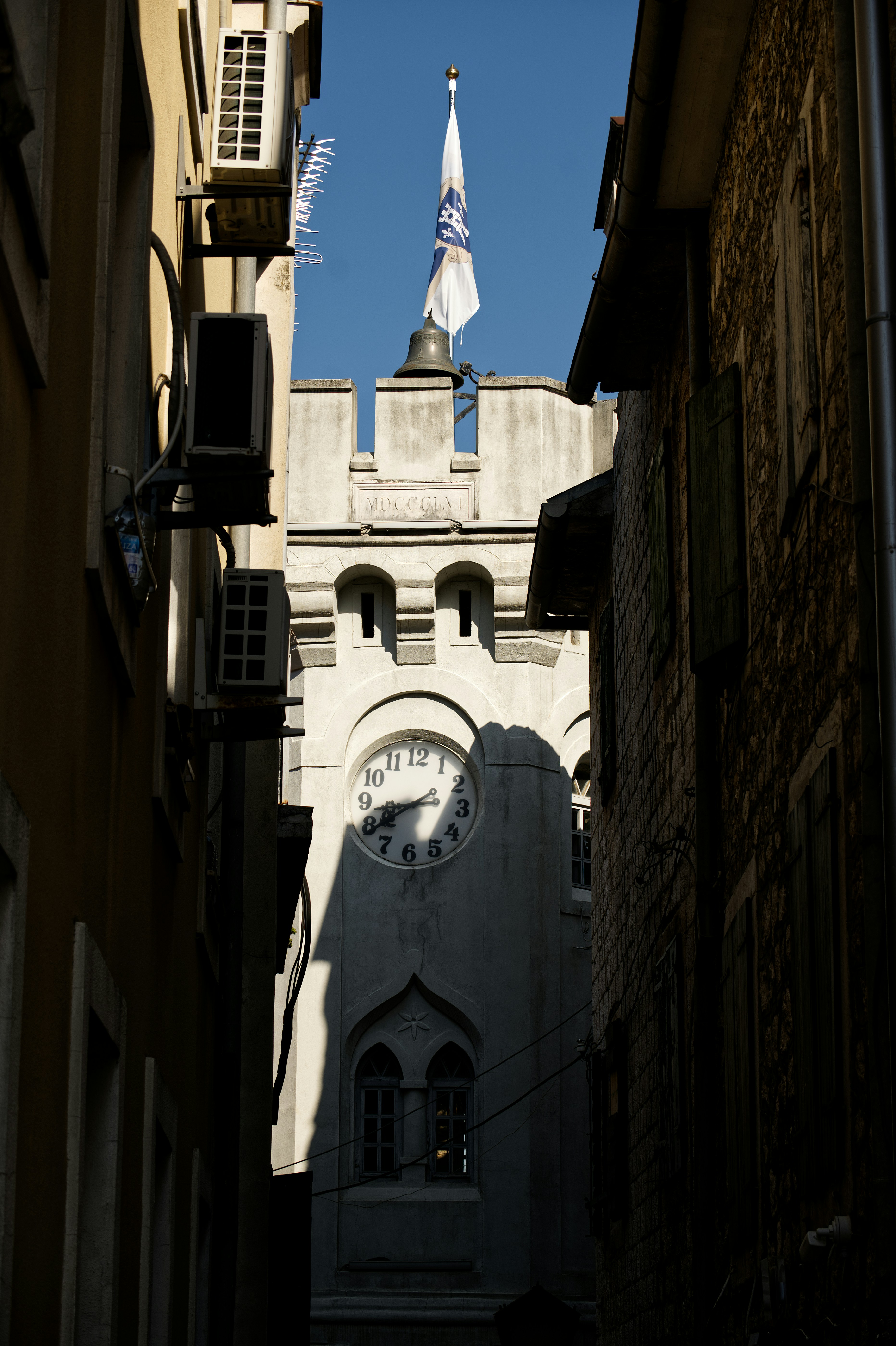 Clock Tower in a Narrow Alley Under a Flag at Dusk