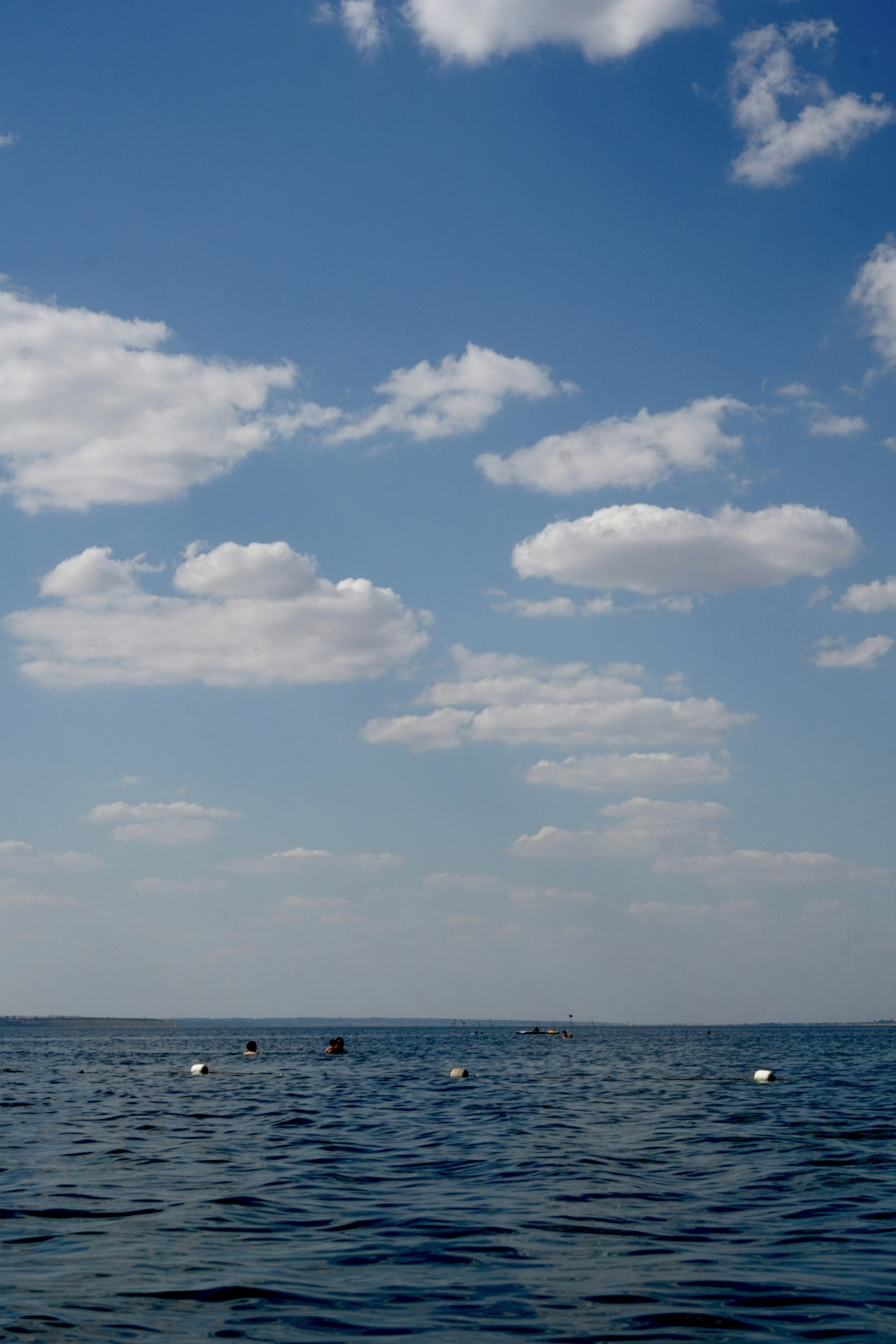 Wide sea and sky scene with distant swimmers near the horizon, calm water textures, minimal foreground detail.