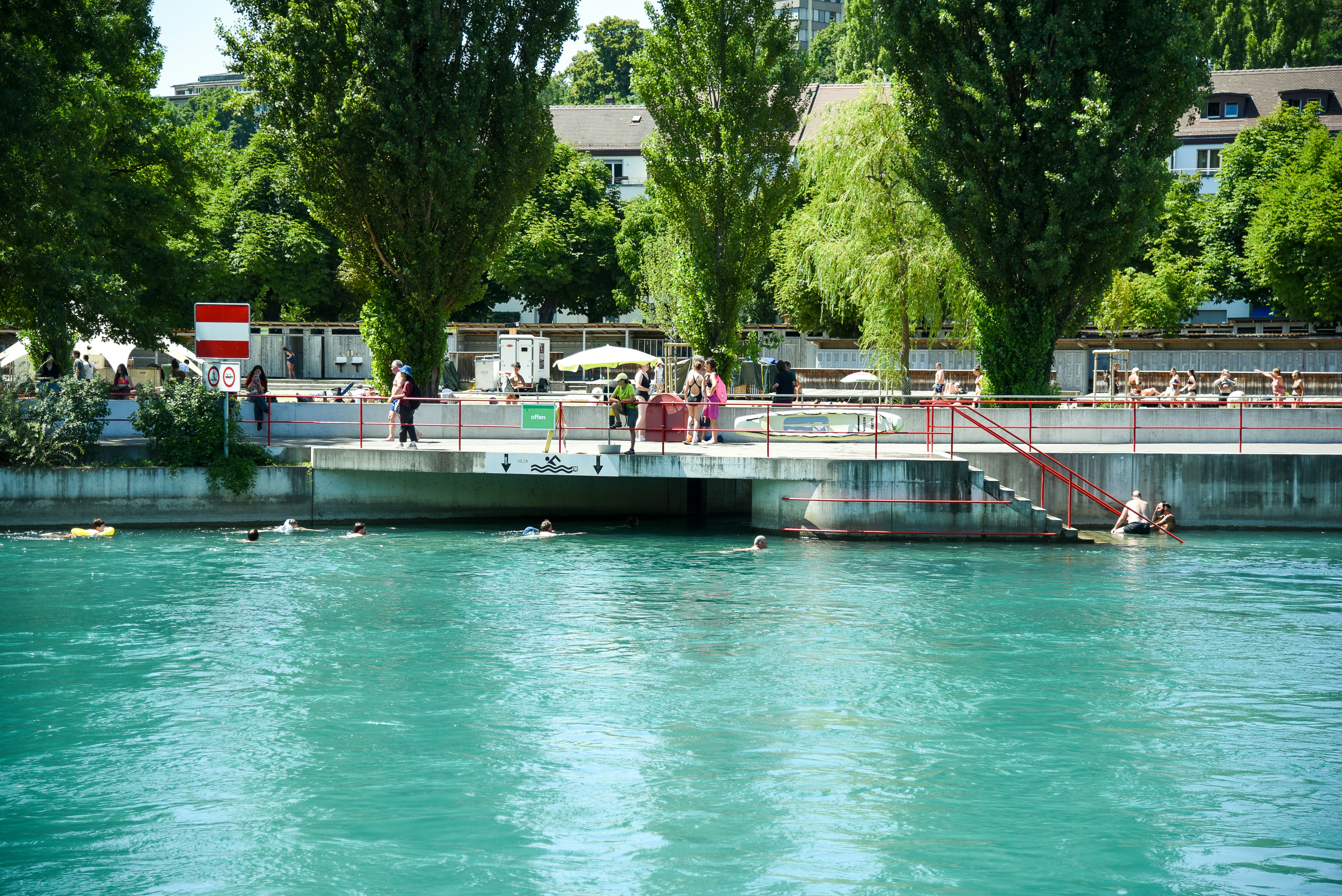 People at a riverside pool under leafy trees