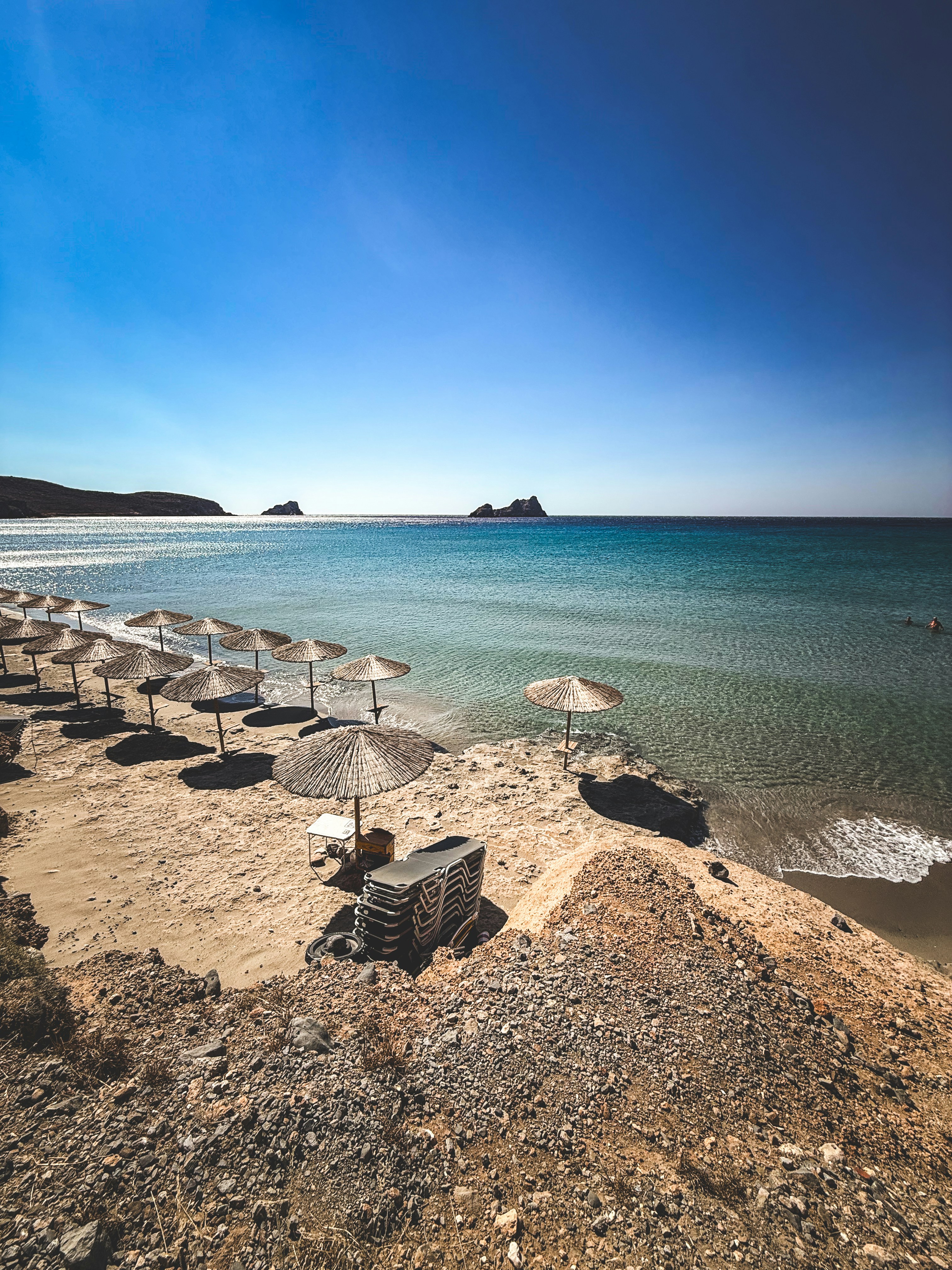 Row of seaside straw umbrellas casting shadows over pebbled beach