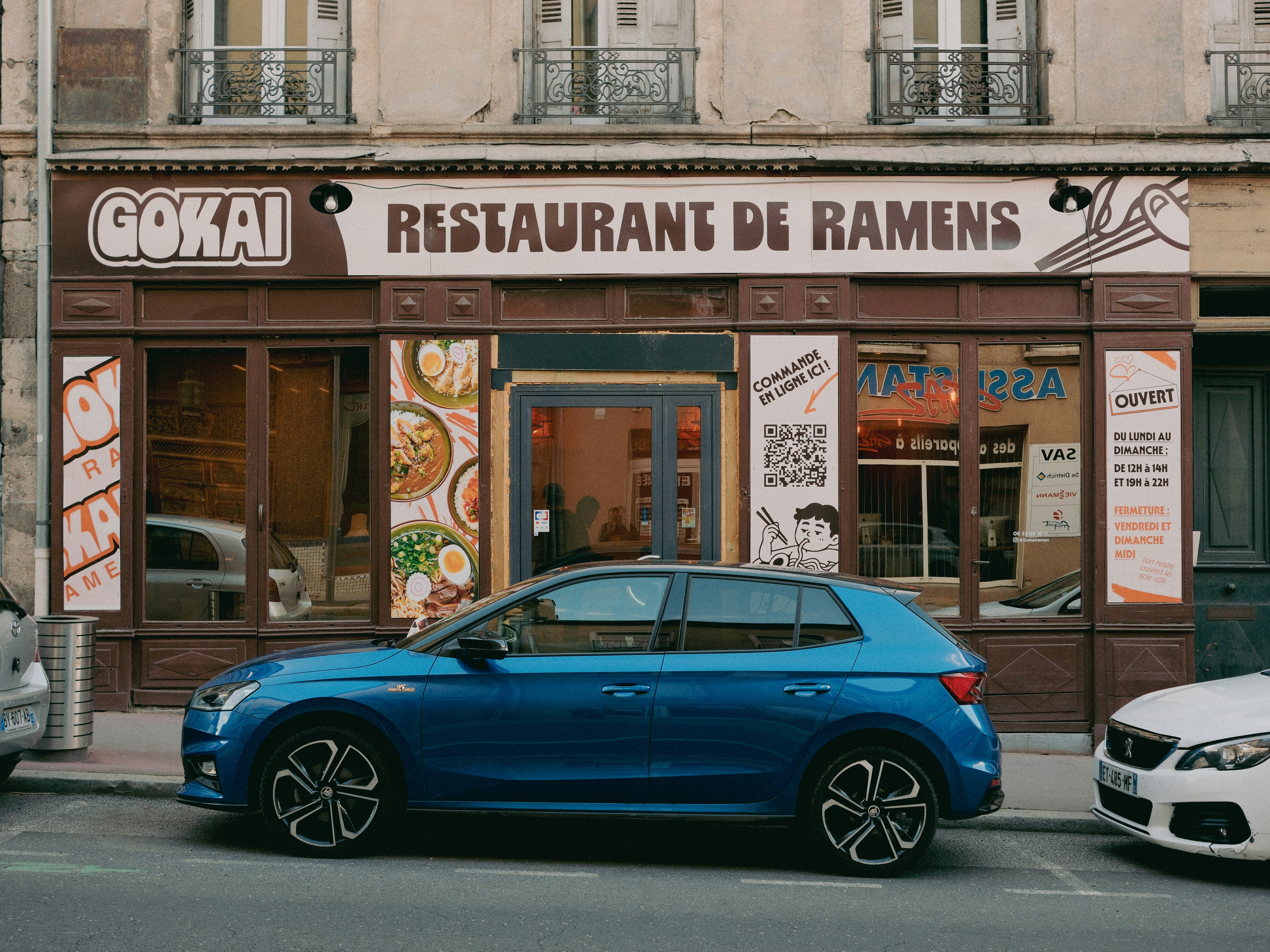 Blue Hatchback Framed Along a Parisian Restaurant Façade