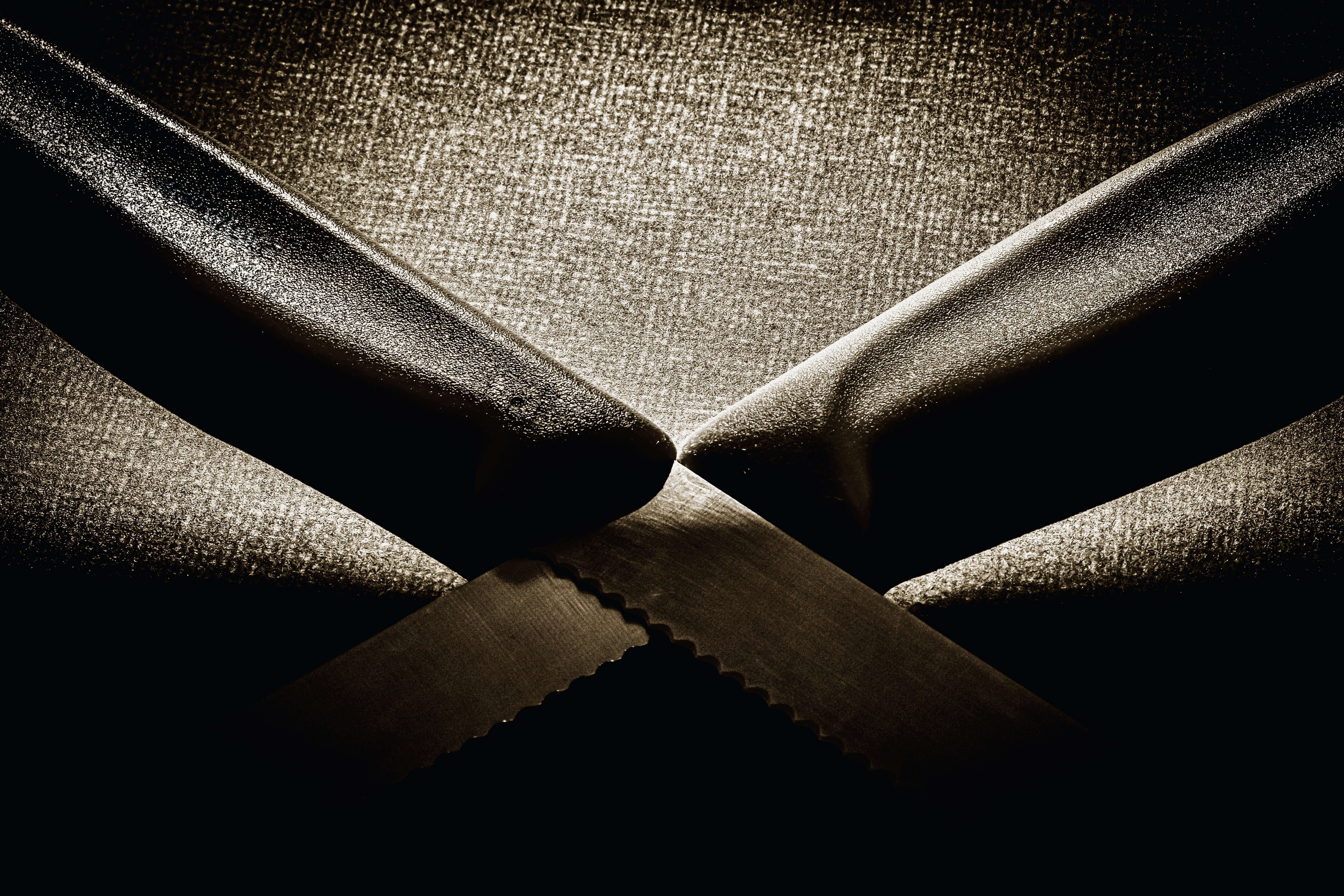 Two pocket knives cross at the blades, silhouetted by a single directional light to reveal the textures of the blades and handles.