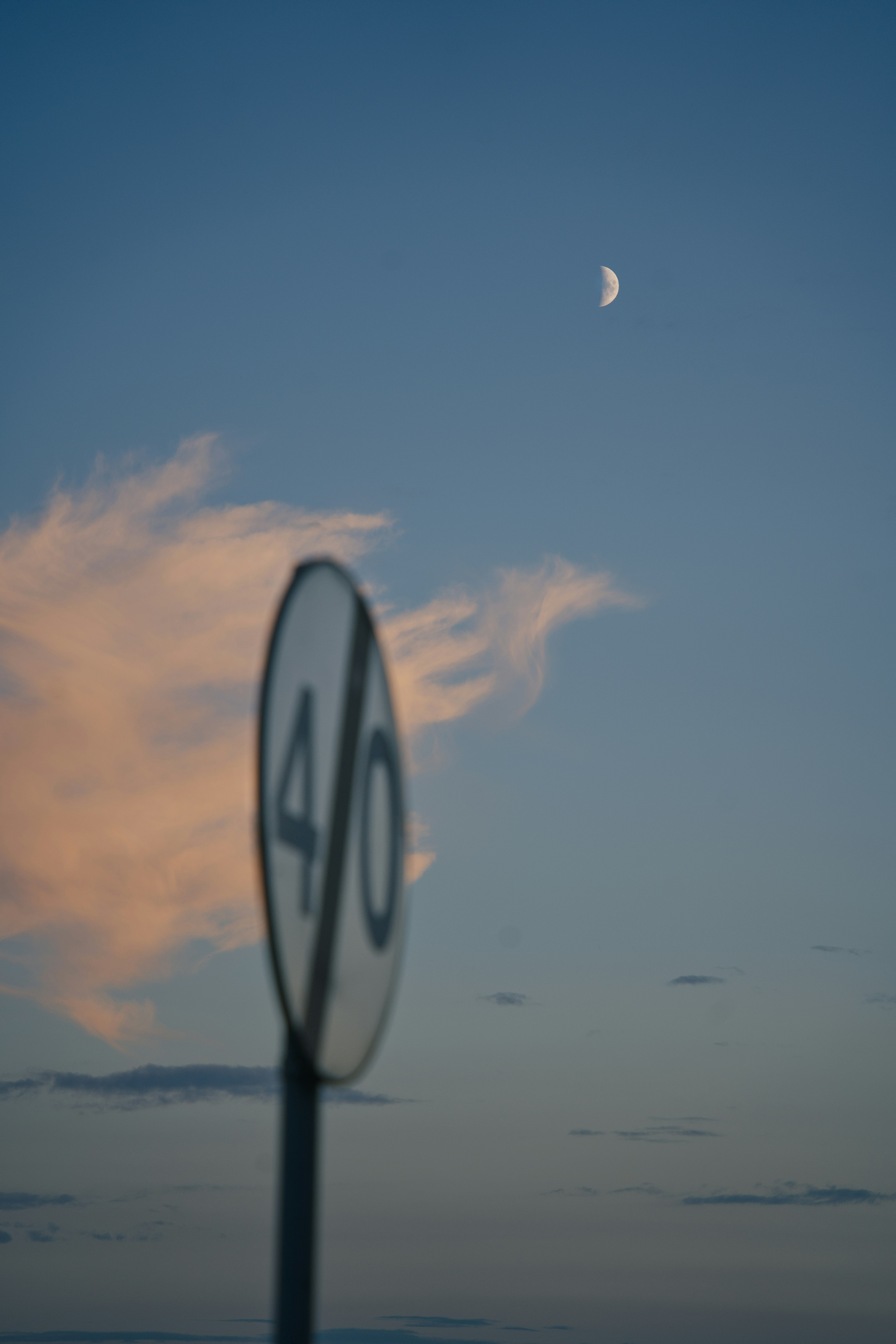 Moon Above the Blur: A Tilted Sign Against Evening Sky