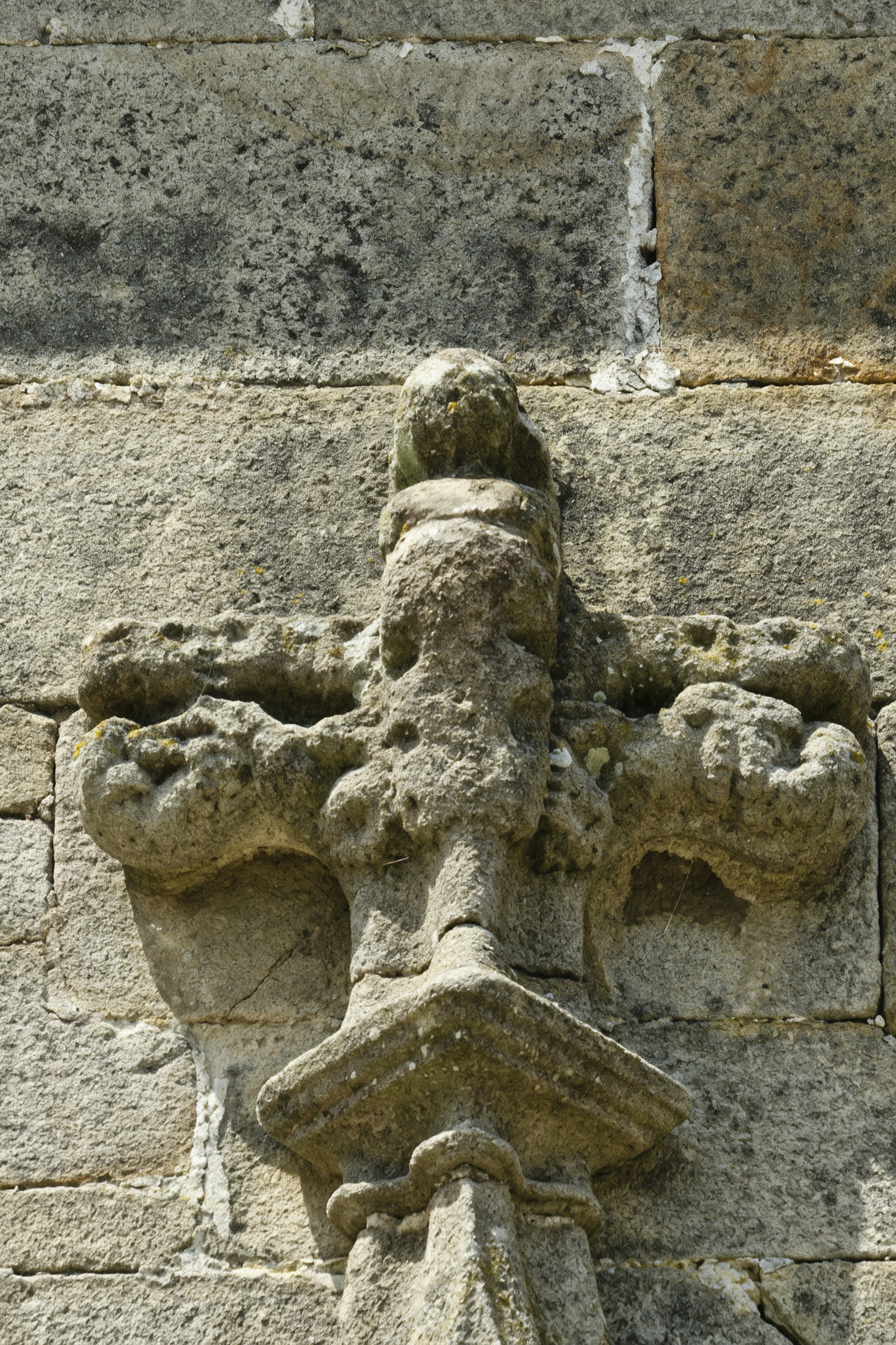 Close-up of an ancient stone cross embedded in a rough brick wall, revealing worn carvings and patina that hint at centuries of exposure.