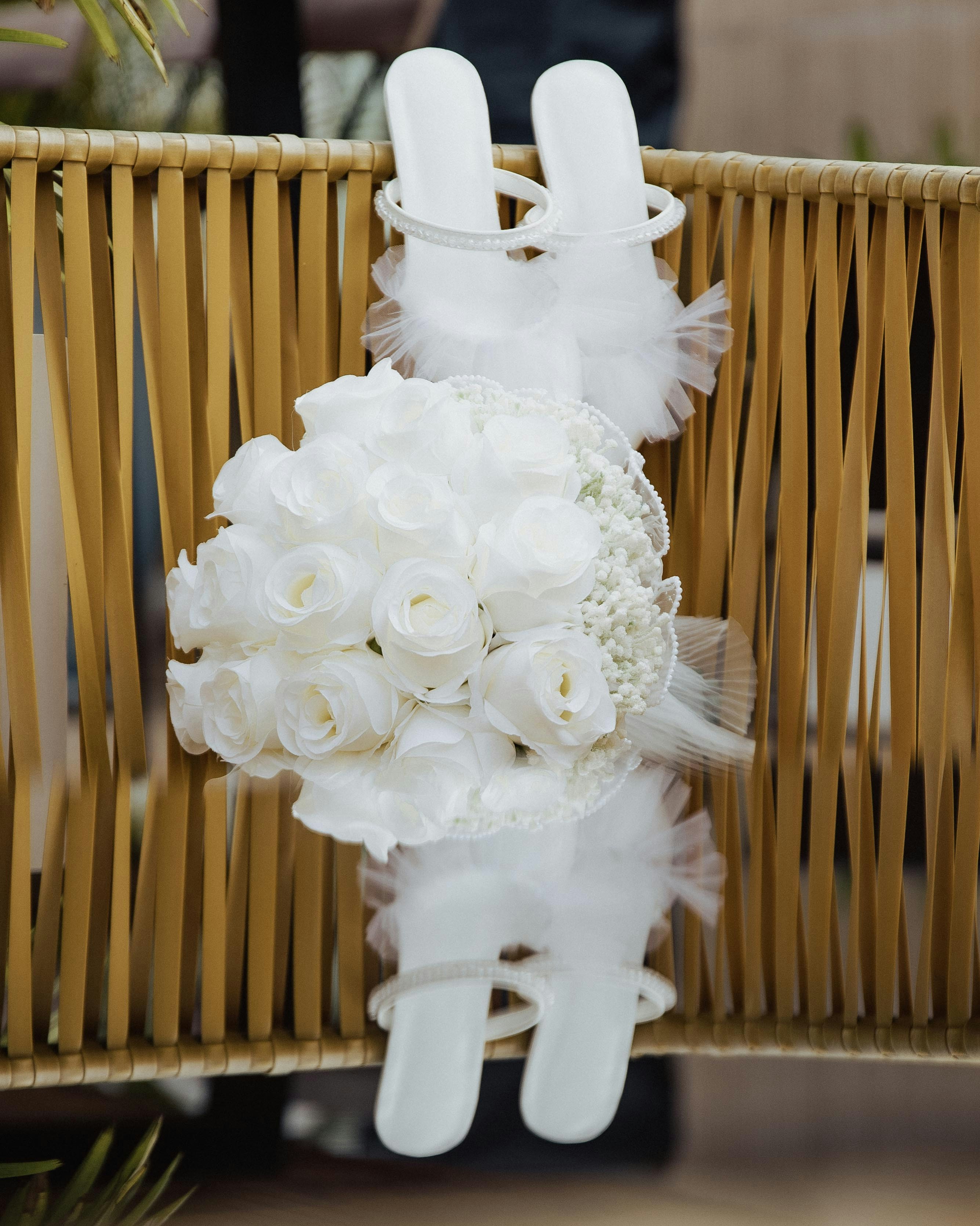 White bouquet on a woven chair: wedding detail with delicate slippers reflection