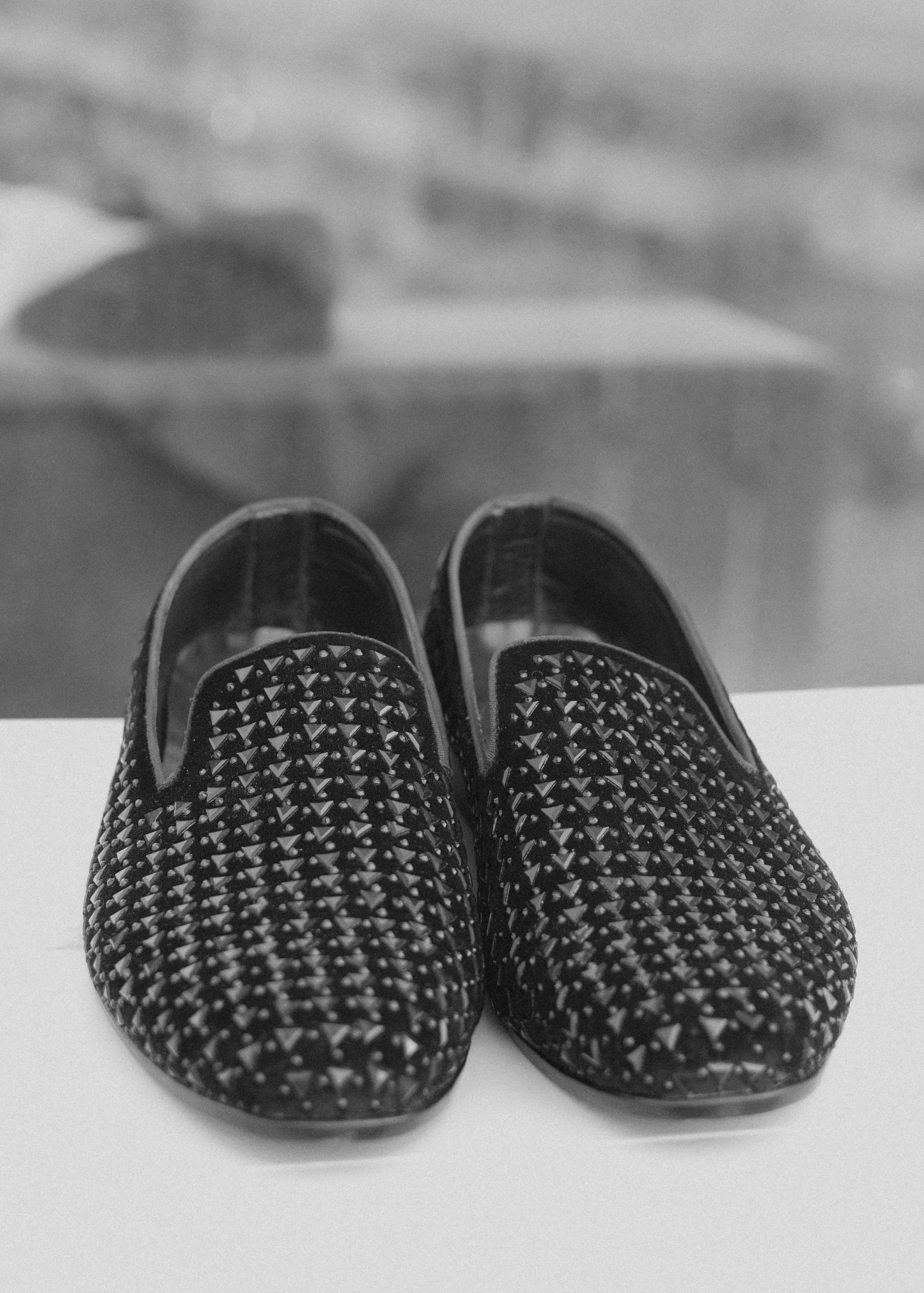 Spiked Steps: Black Slip-Ons Resting on a White Glassy Surface