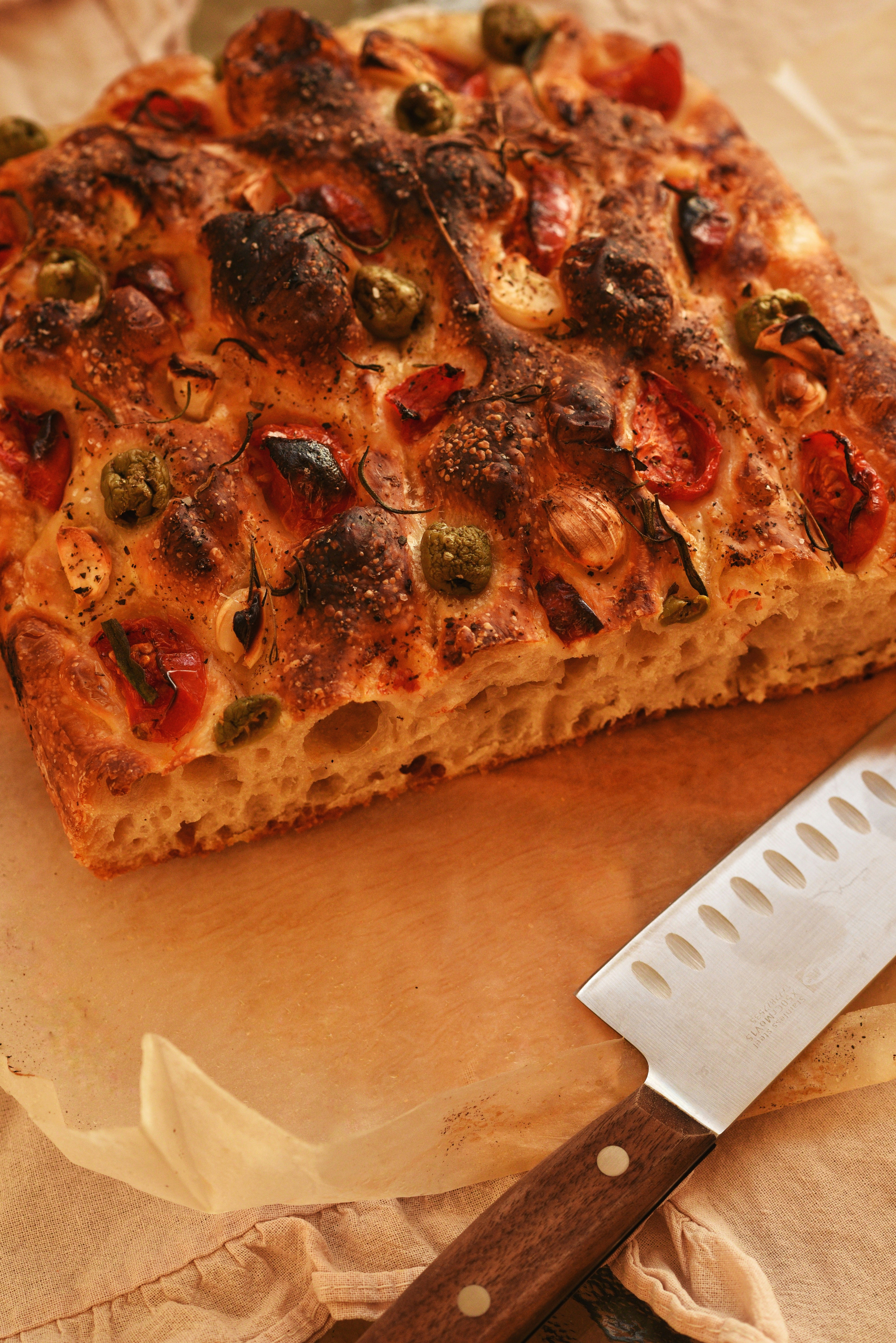 Olive-olive scented focaccia loaf with charred edges and peppered crust