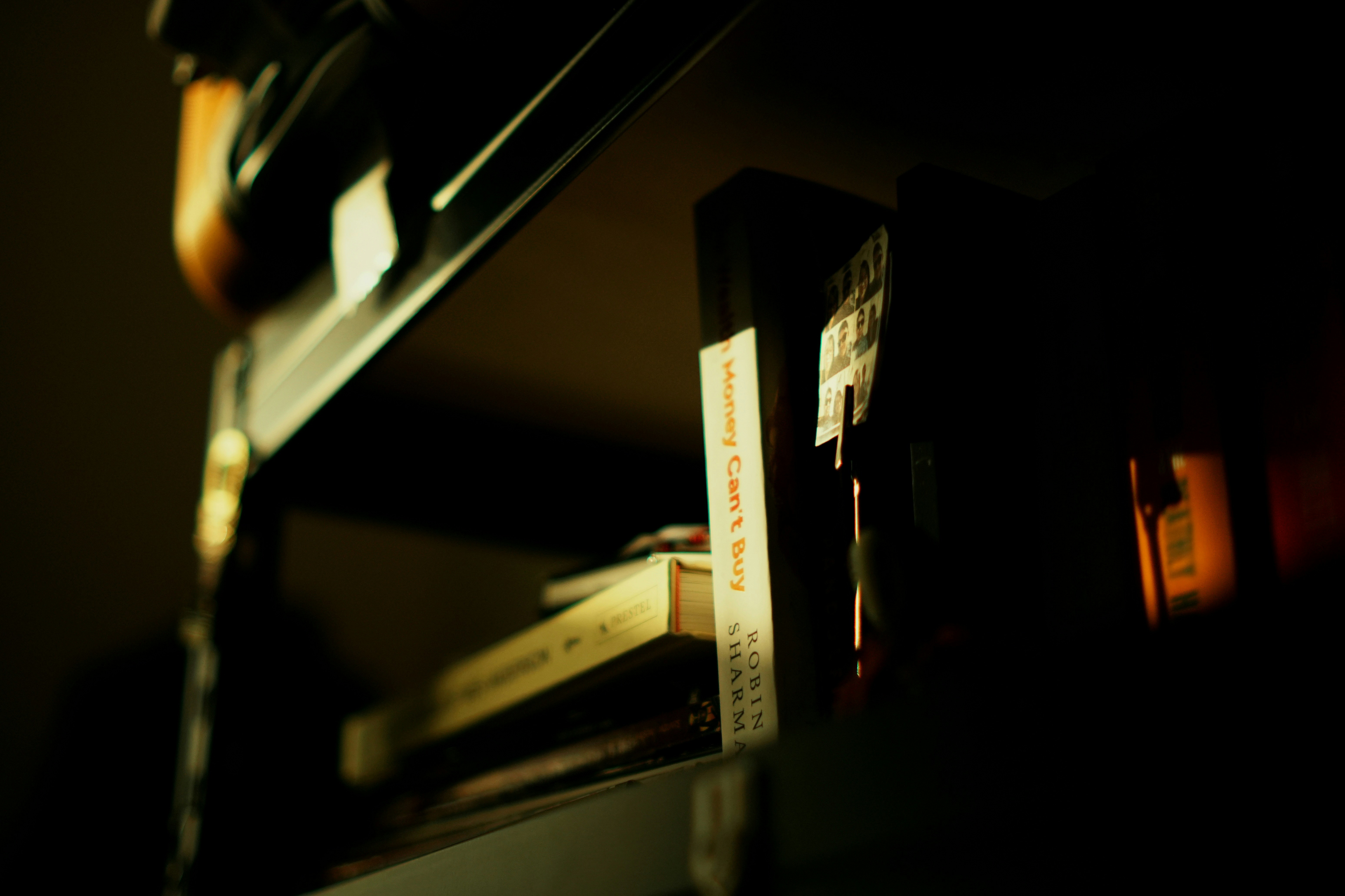 Dimly lit shelf with books and a few objects, the brightest spine near the center creating a subtle focal point and mood.