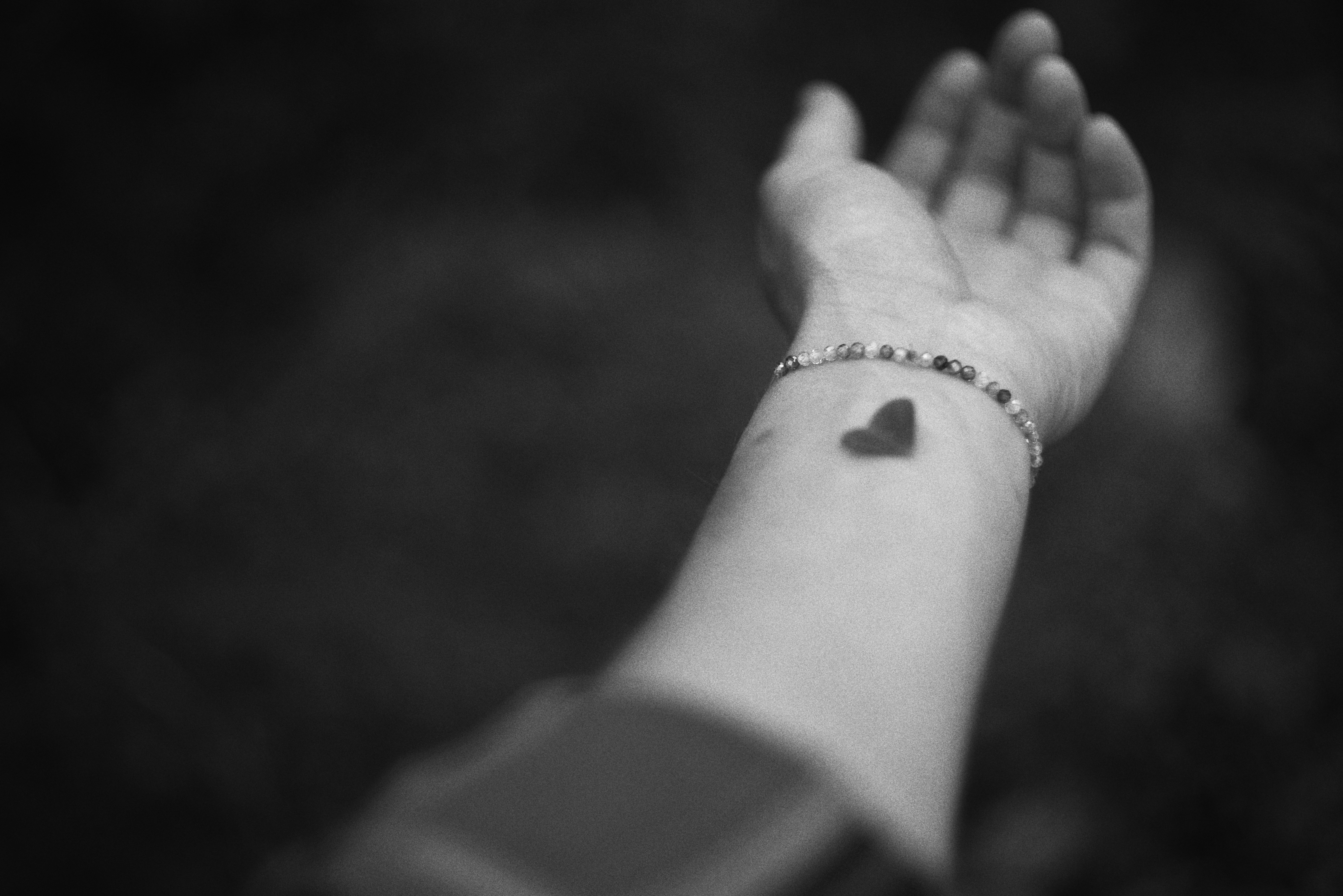 Heart tattoo, bracelet, and outstretched arm in soft-focus monochrome