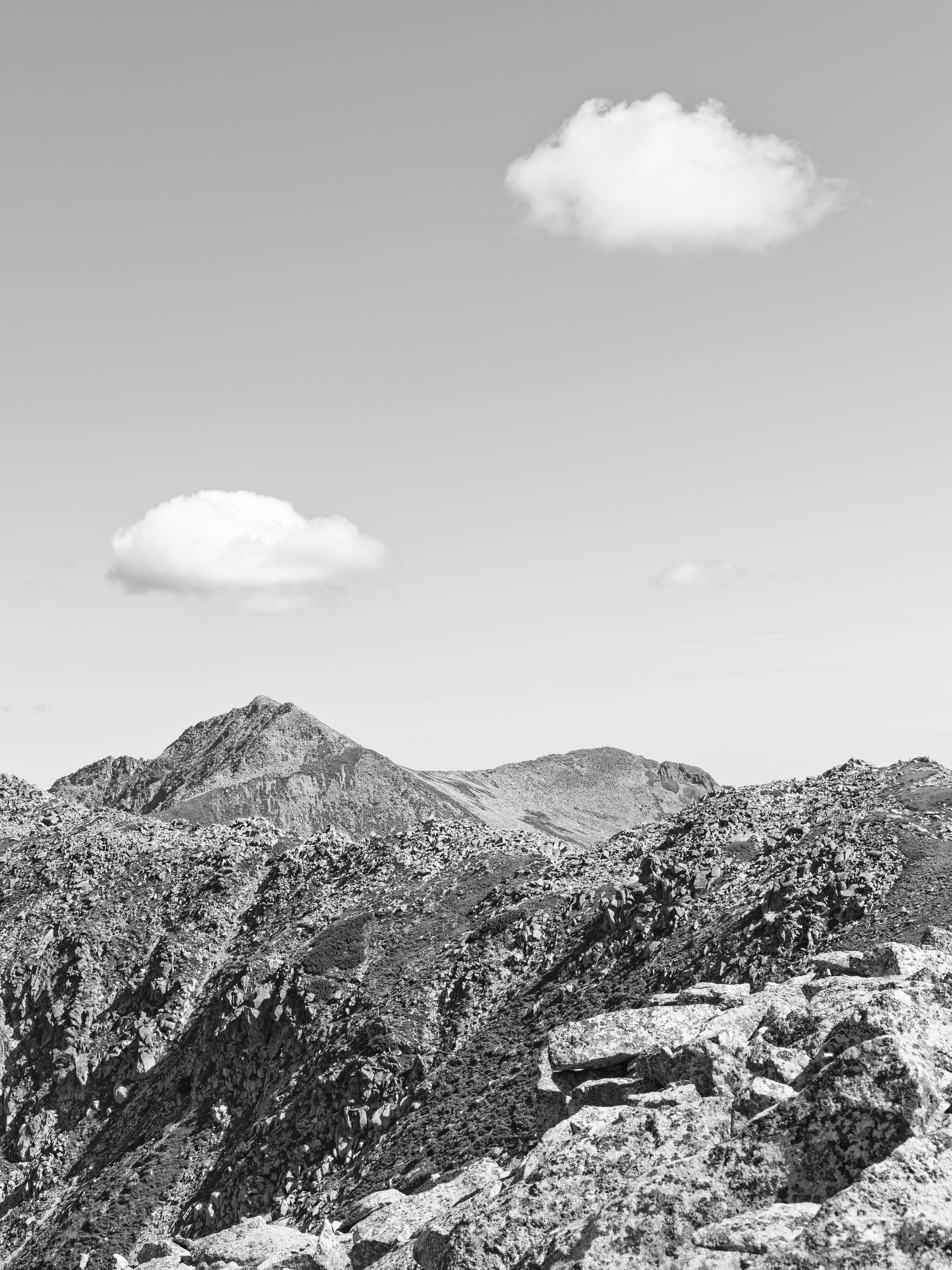 Monochrome rugged mountain ridge under a pale sky with scattered clouds, emphasizing texture and depth of the rocky terrain.
