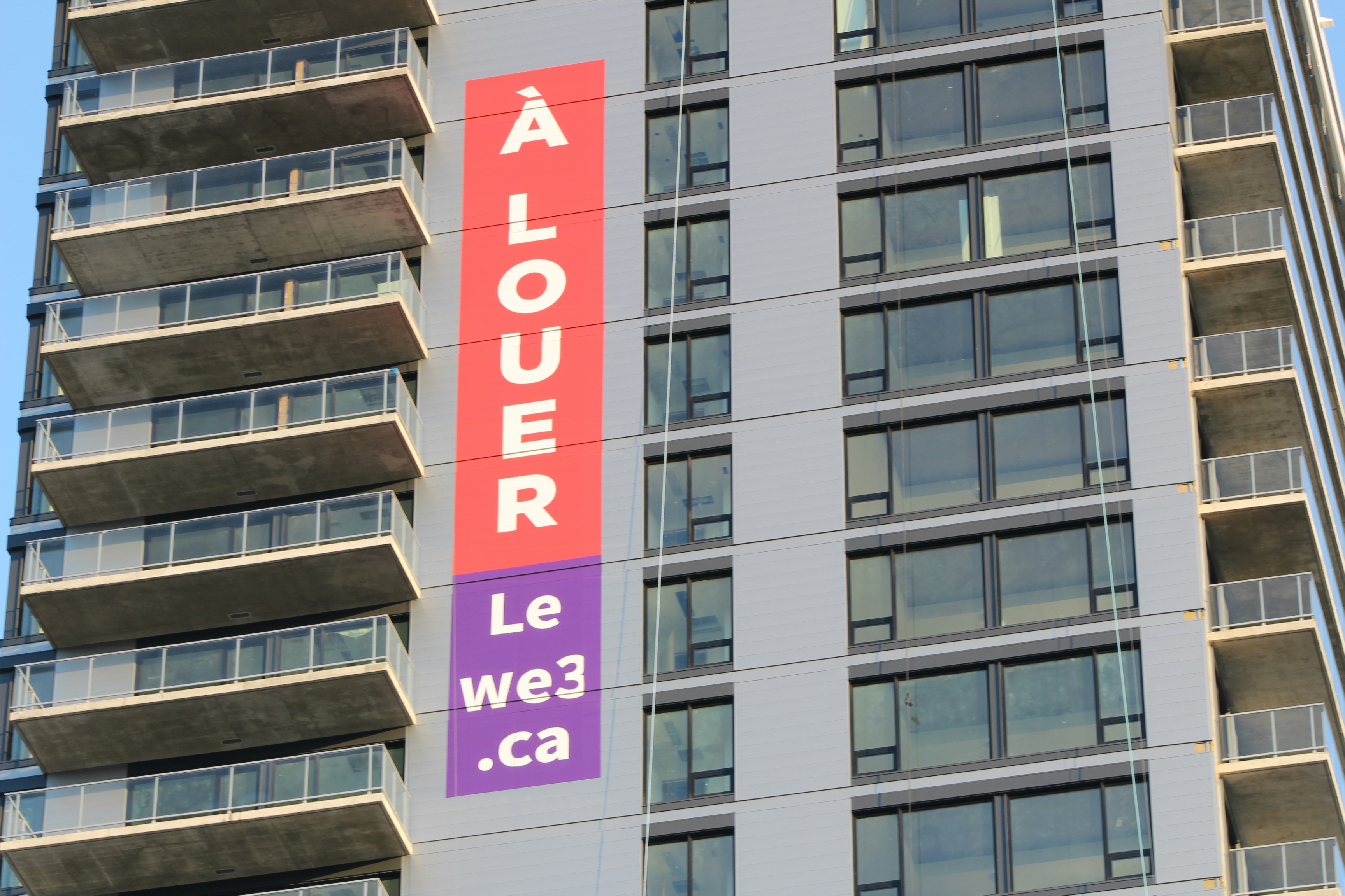 Vertical For Rent: A Bold Red and Purple Sign Adorns a Modern Glass-Fronted Building