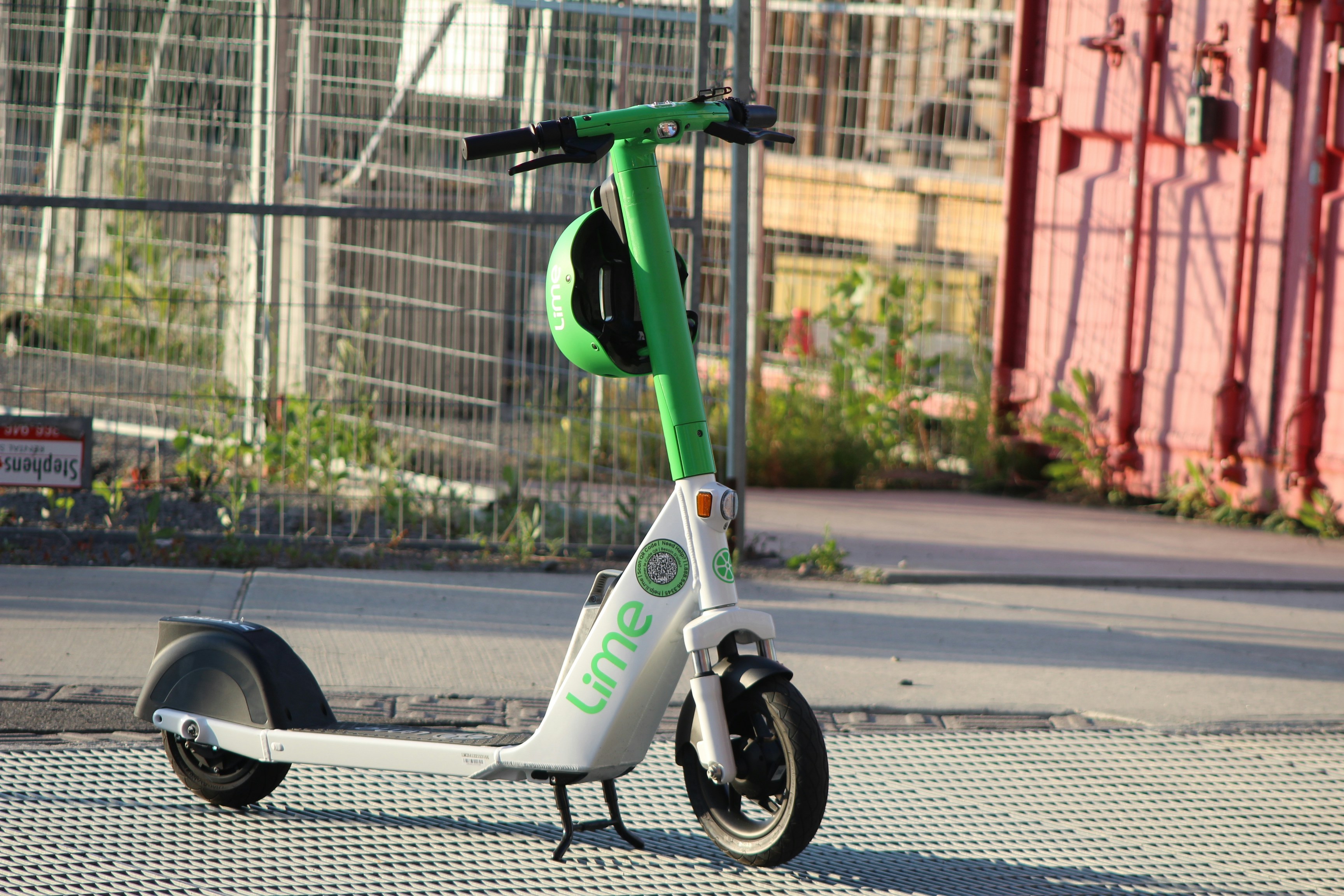 Lime electric scooter parked at the curb with urban fencing in the background