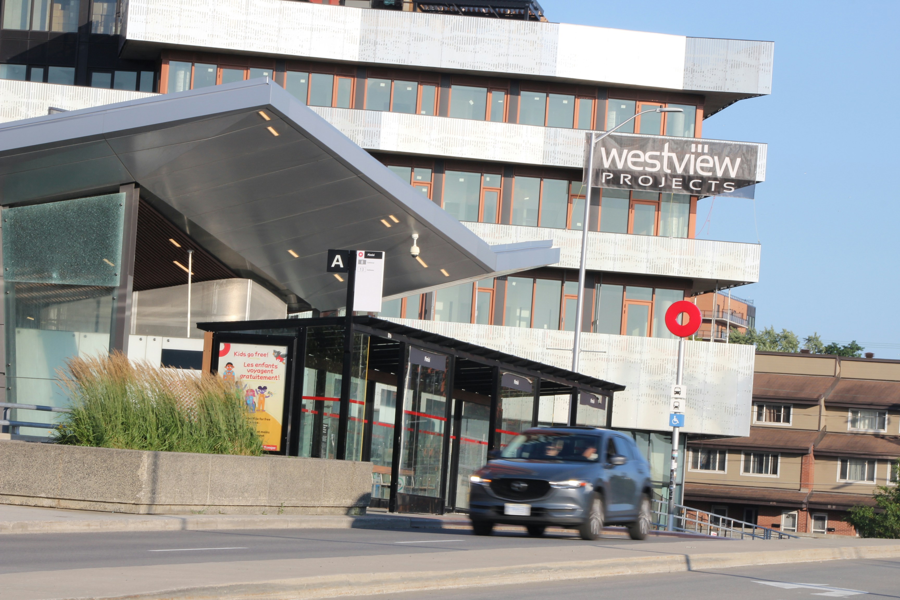 Modern building entrance with glass canopy and a Westview Projects sign, car passing by on the street; architectural detail and urban transit scene captured at an angle.