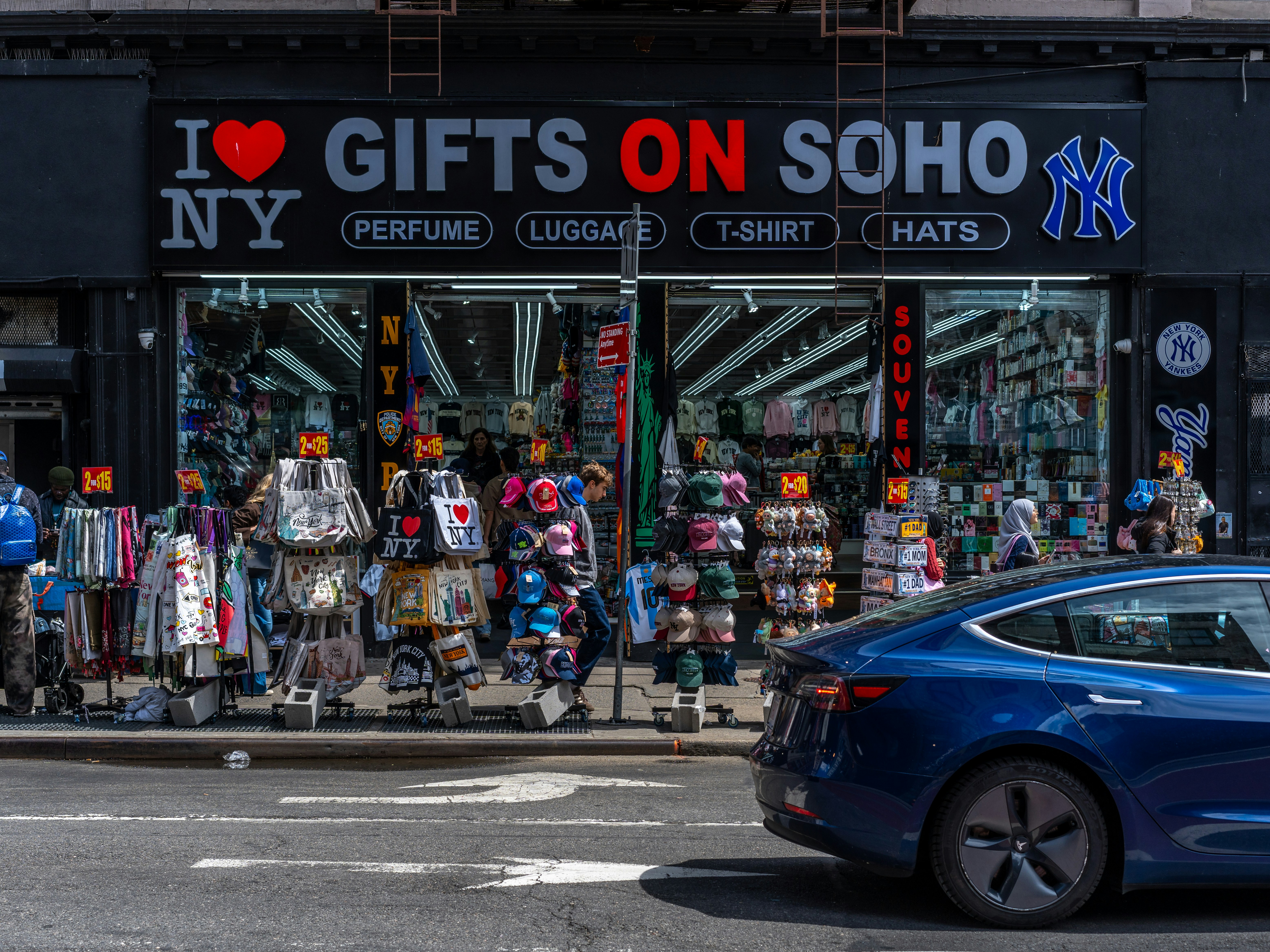 Neon storefront in Soho: a busy souvenir hub framed by a passing blue EV