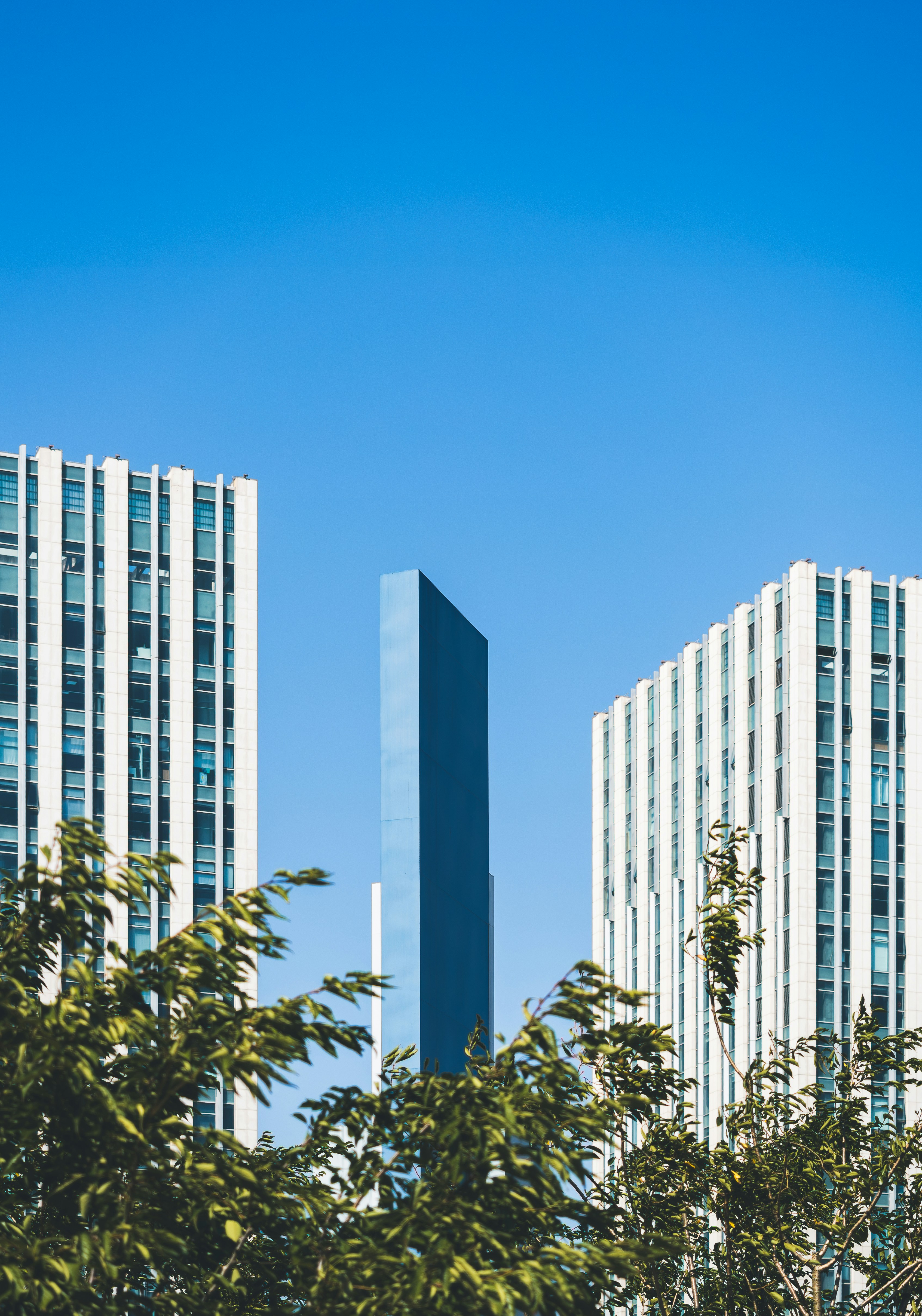 Central Skyward: A Blue Obelisk Between Twin Urban Pillars
