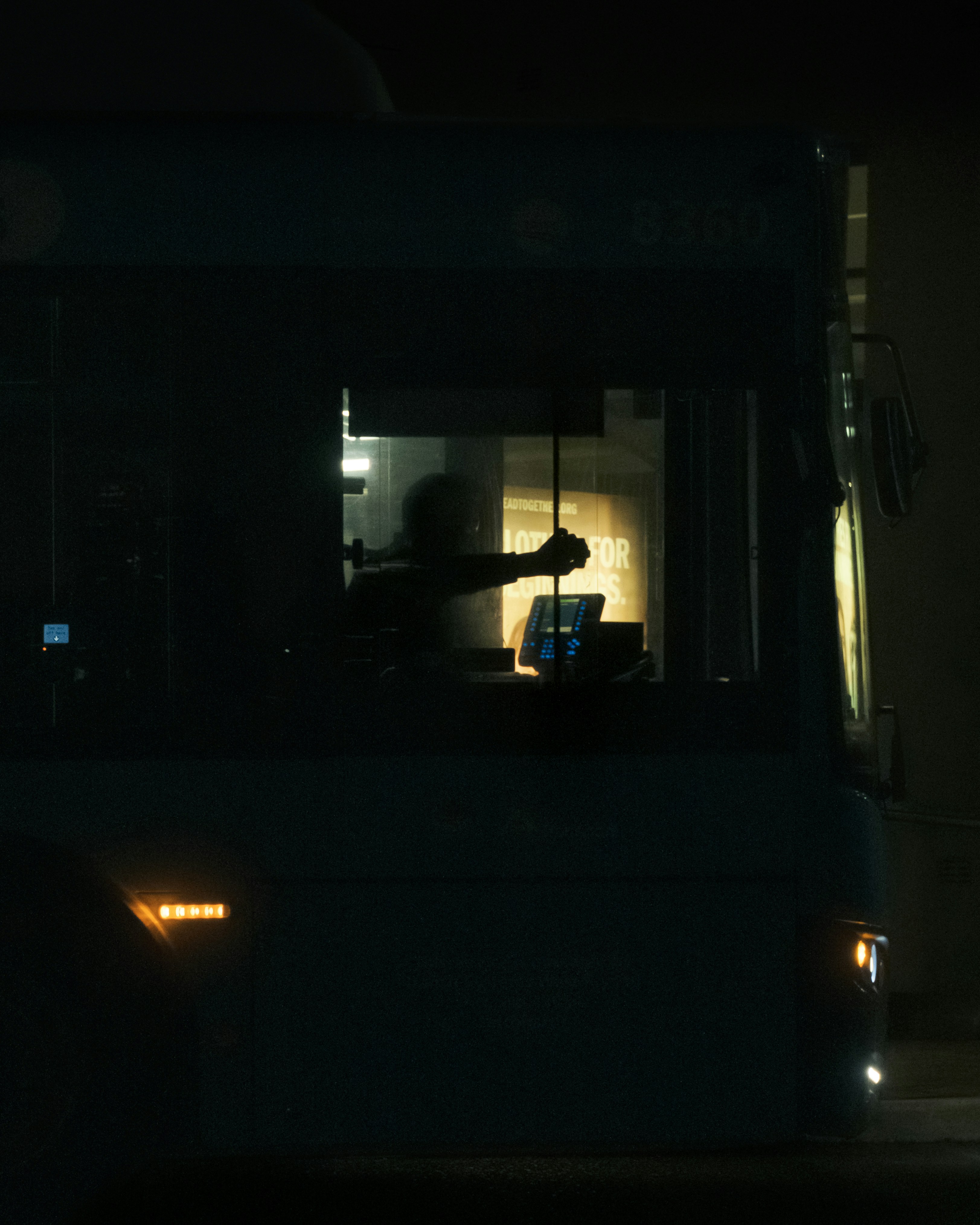 Night Bus Doorway: silhouette of a worker inside a glowing cockpit