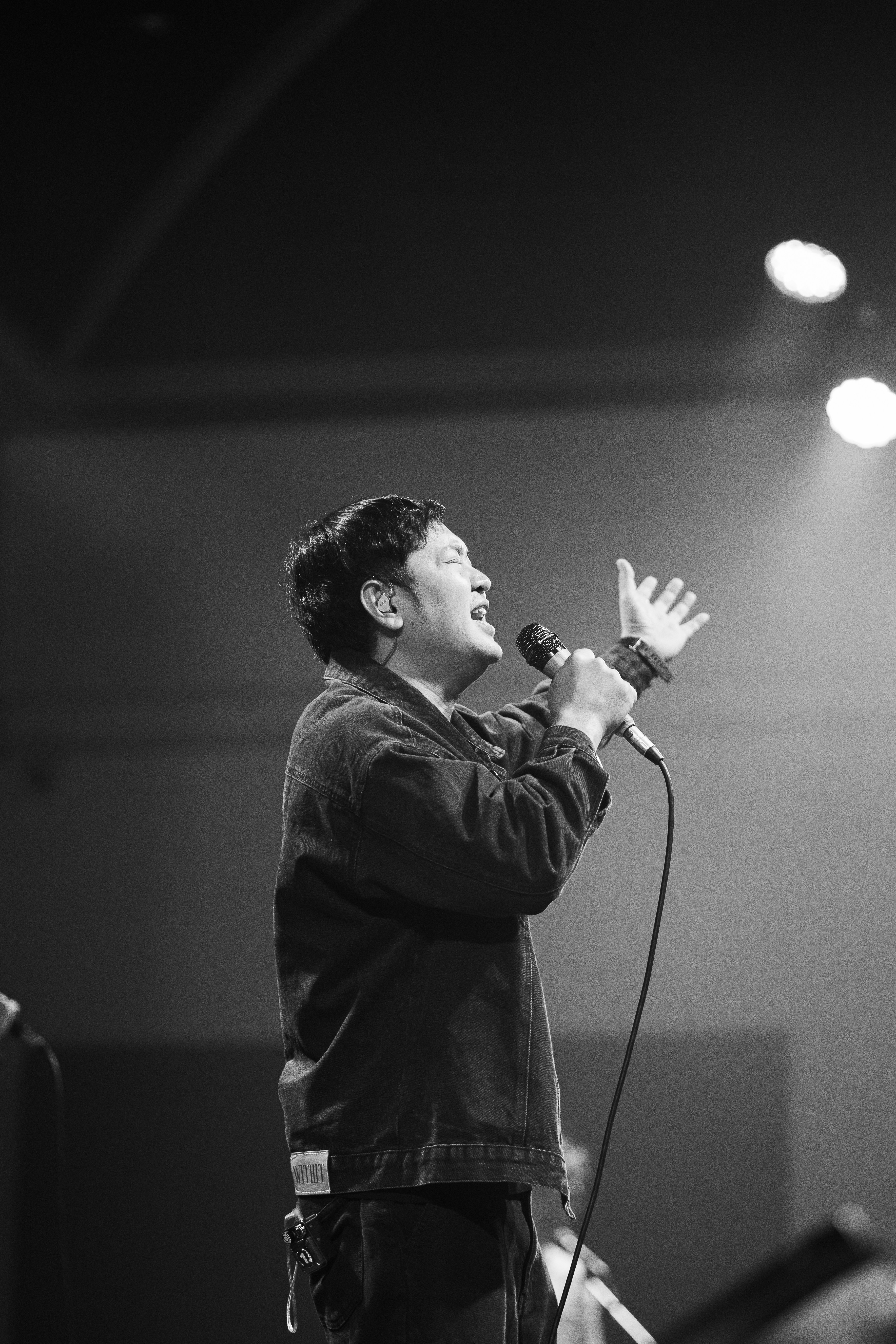 Mid‑solo on a dim stage: a singer in denim belts out emotion