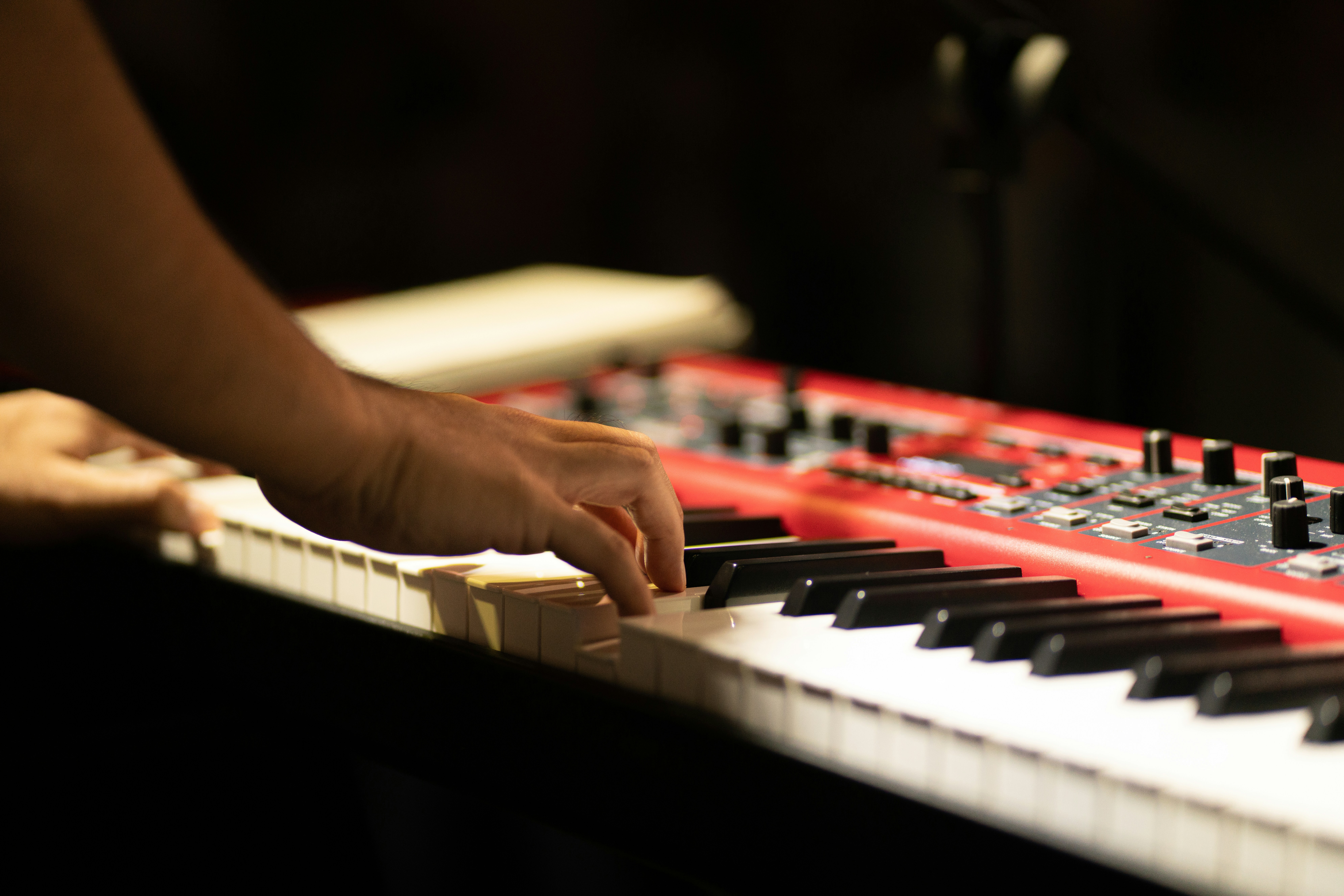 Close-up of hands playing a red electronic keyboard, studio lighting highlighting the keys and fingers as they move across the instrument.